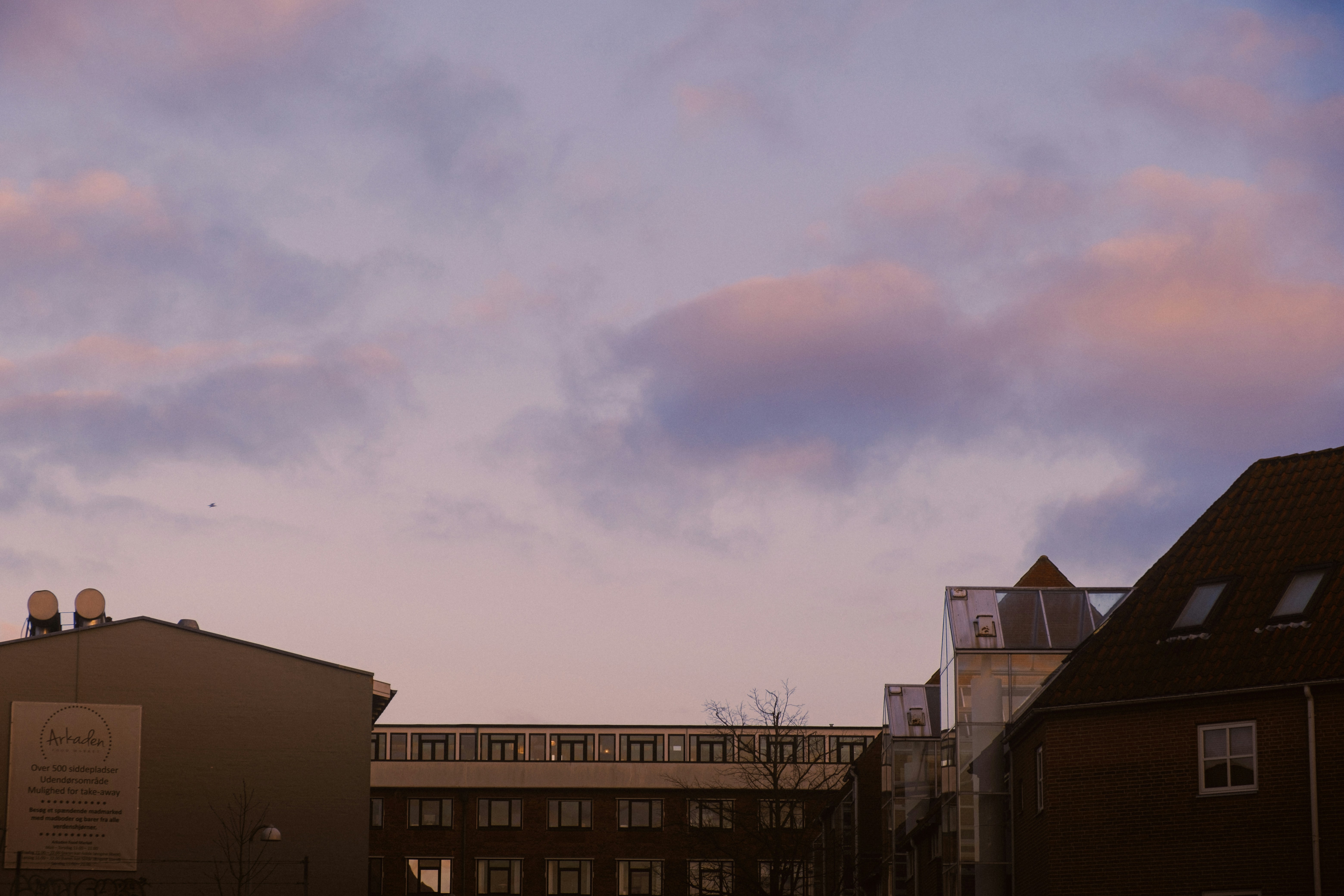 Soft pink clouds float above urban buildings at dusk.