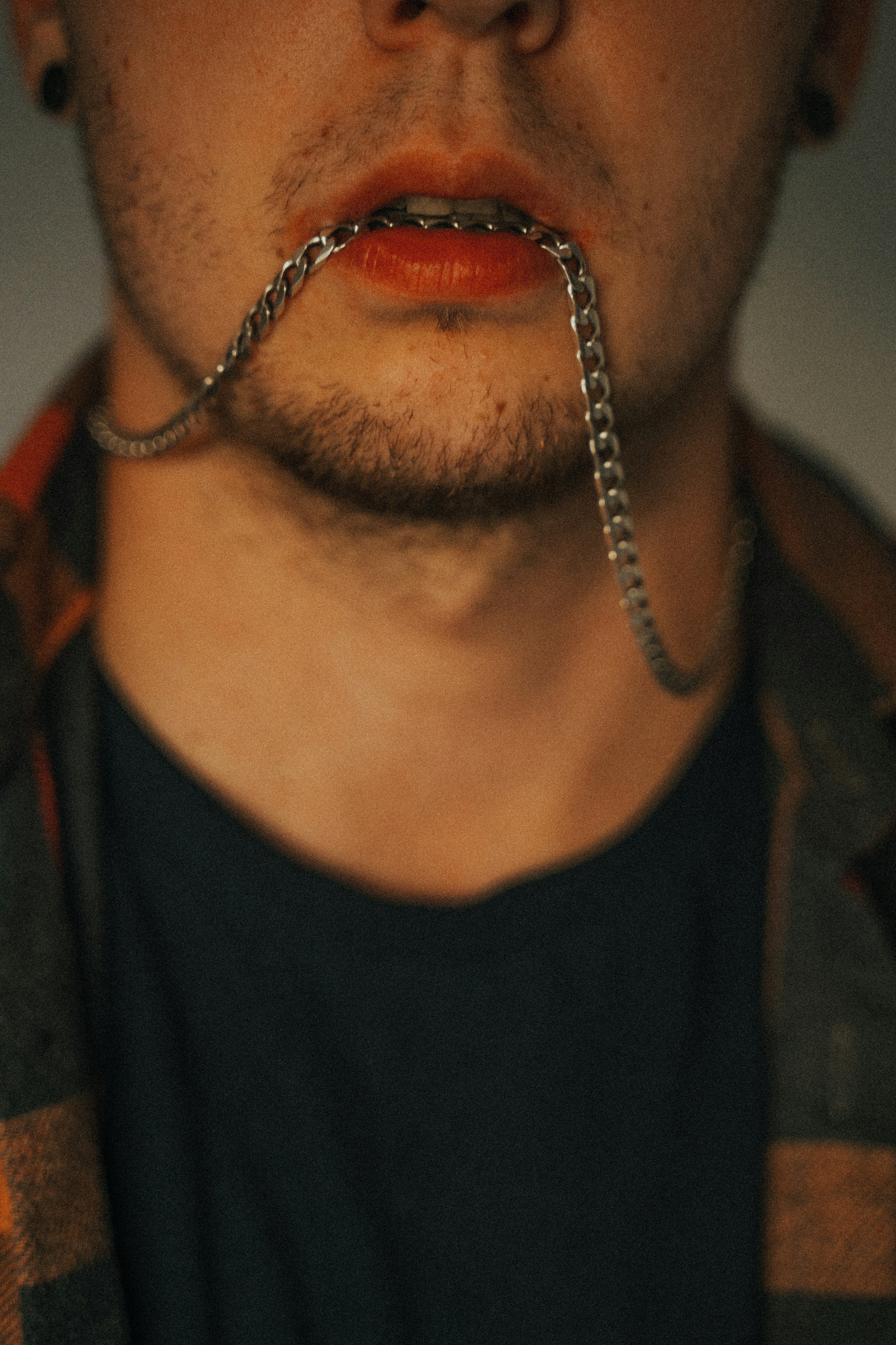 Close-up portrait of a person with a chain in their mouth, conveying a sense of rebellion and individuality.