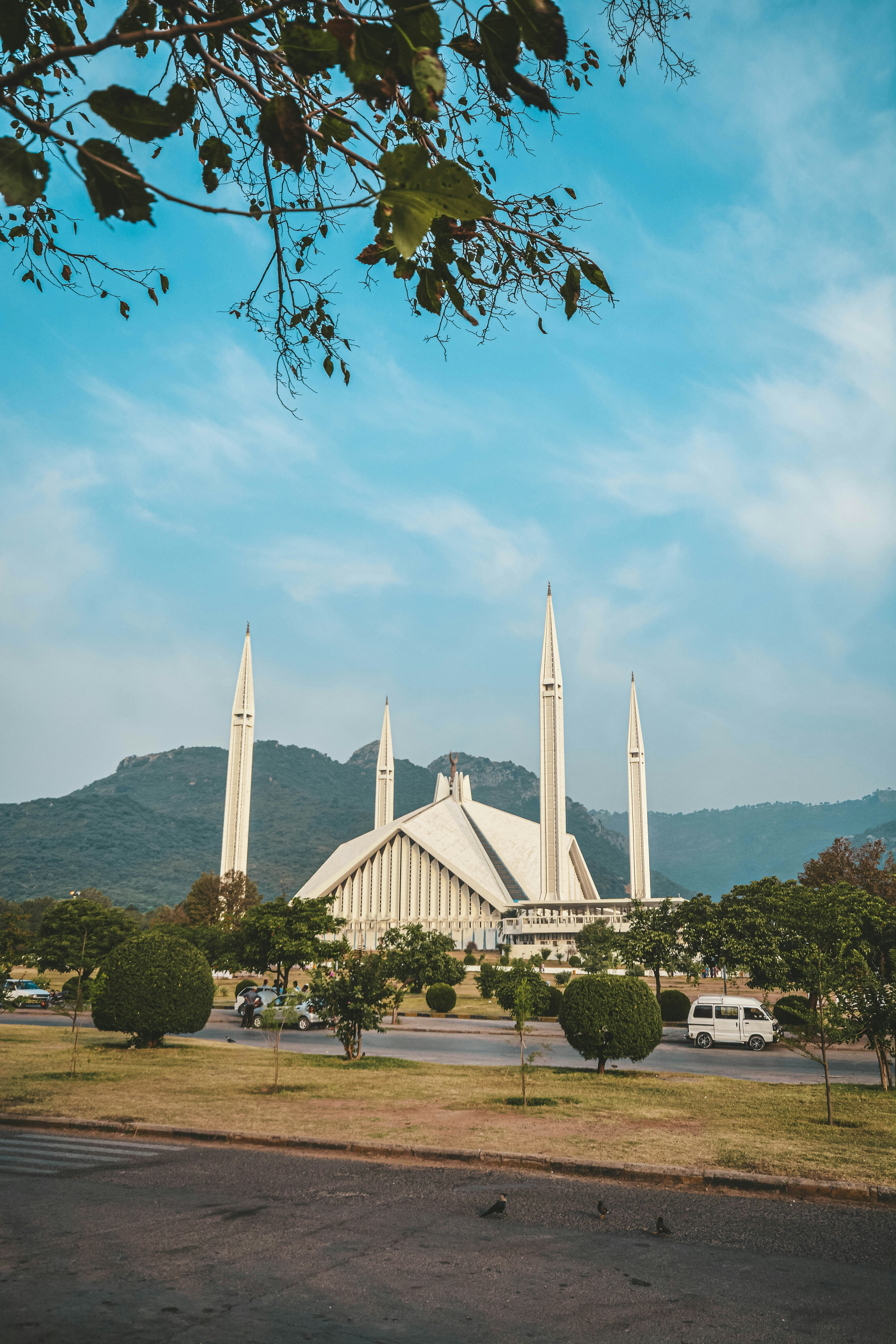 White mosque with tall spires set against a mountain under a clear blue sky.