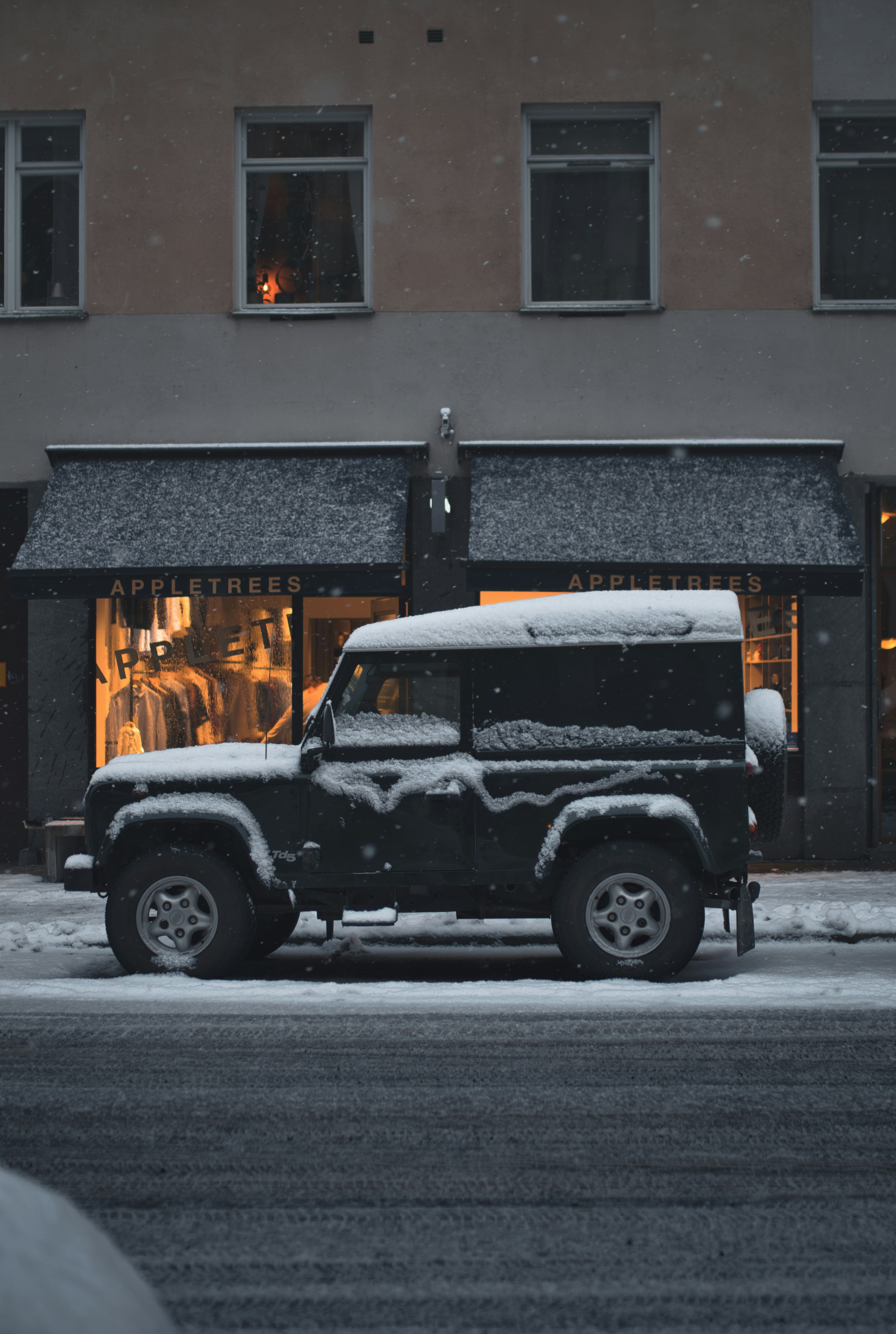 Snowbound SUV Framed by Amber Storefronts on a Quiet Winter Street
