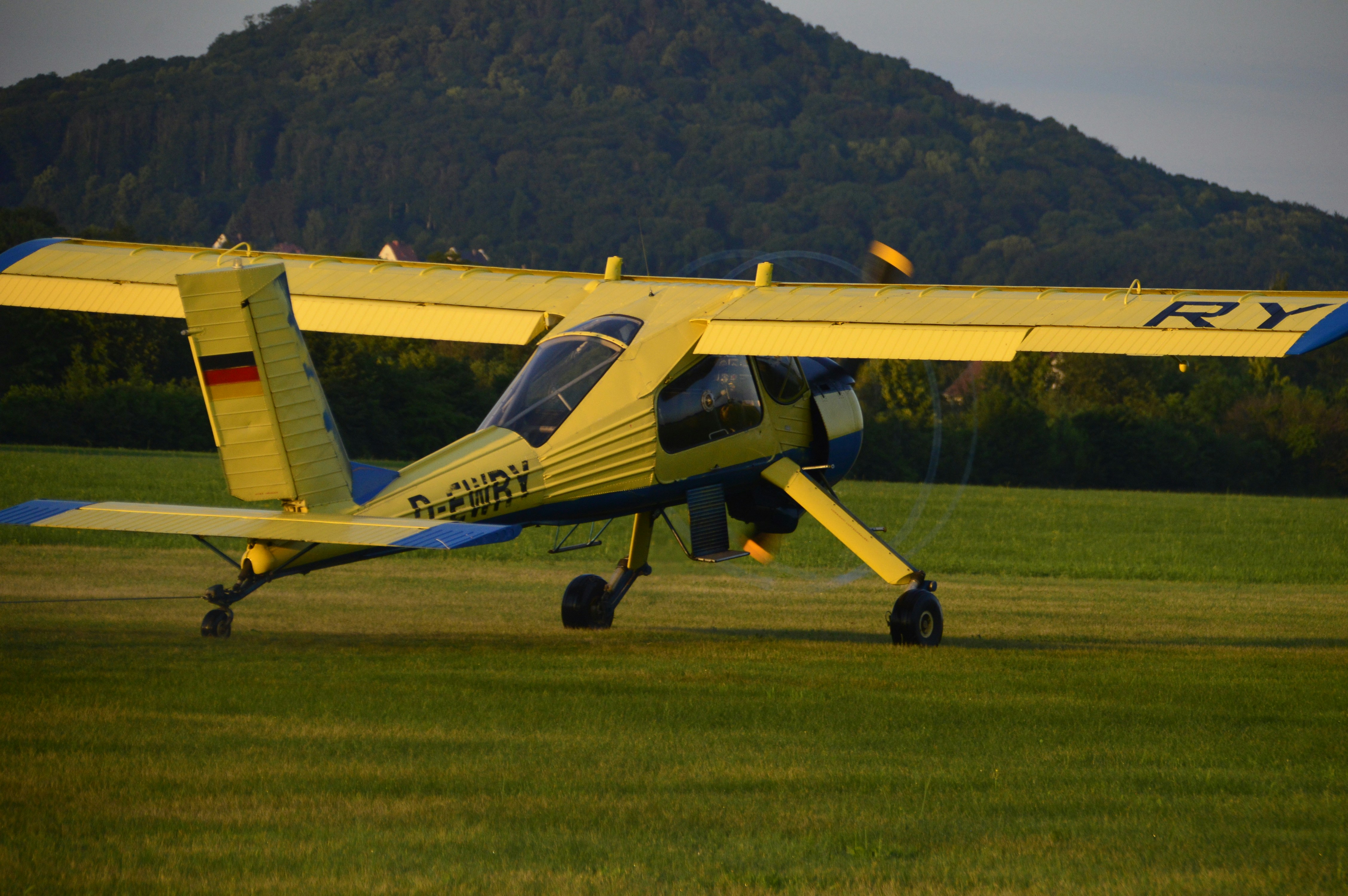 Sunlit Yellow Plane on a Quiet Grass Runway, with Forested Hills in the Distance