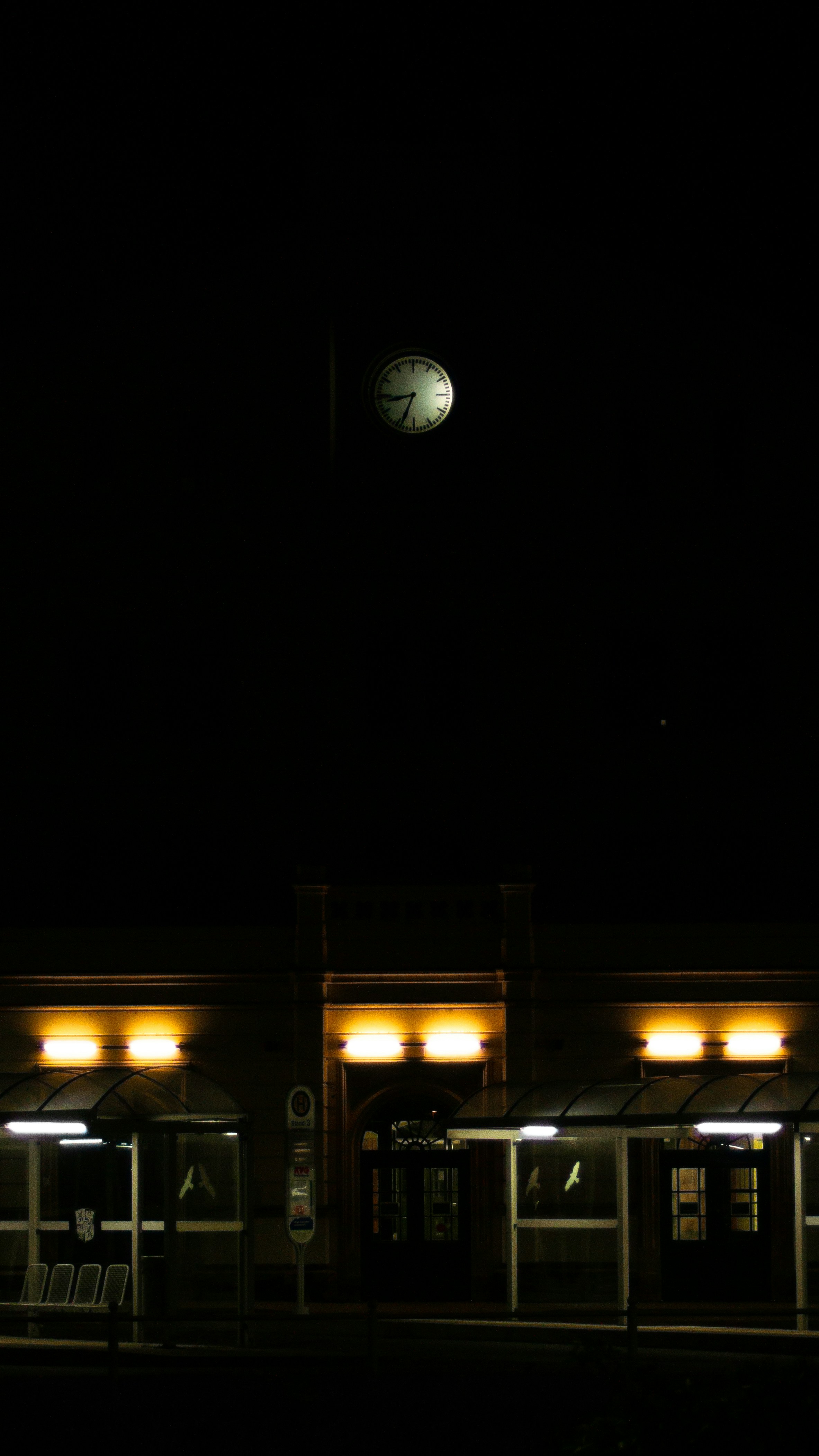 Illuminated clock tower against a dark backdrop, highlighting the passage of time in a quiet urban setting.