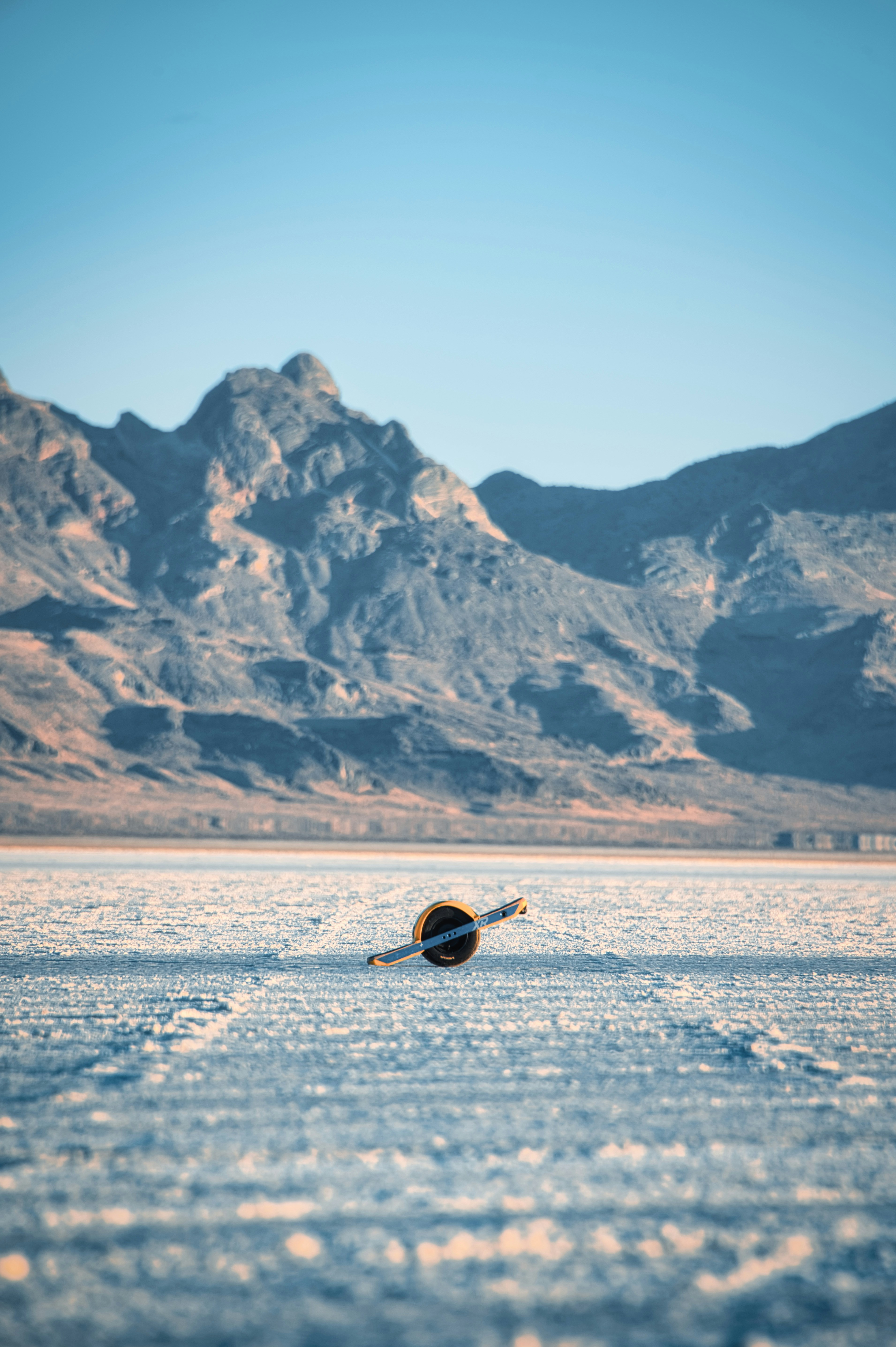 Salt-Flat Sentinel: A Lone Wheel Anchors a Vast Icy Plane Beneath Jagged Peaks