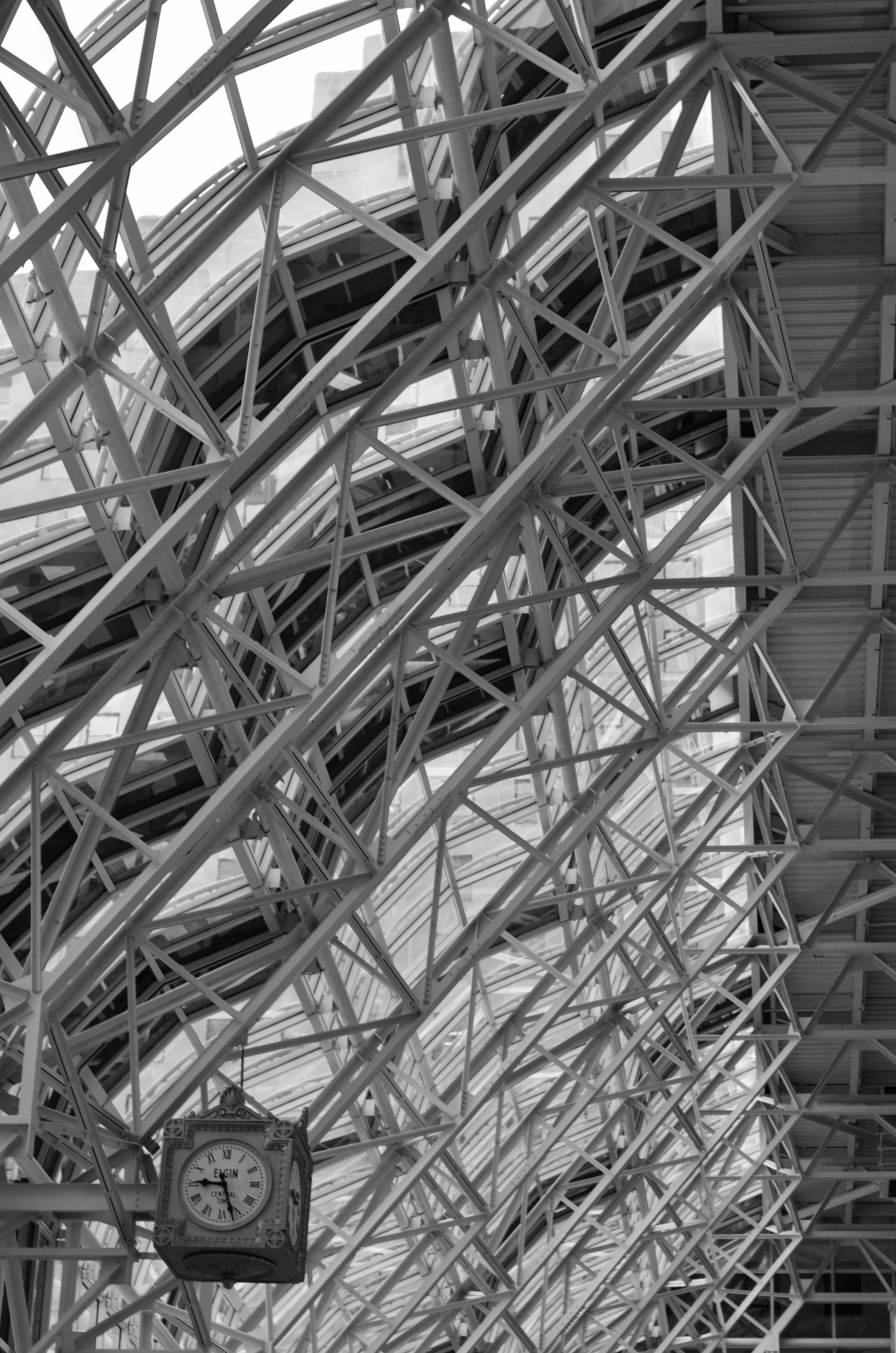 Vintage clock suspended amidst a web of modern architectural beams and skylights.