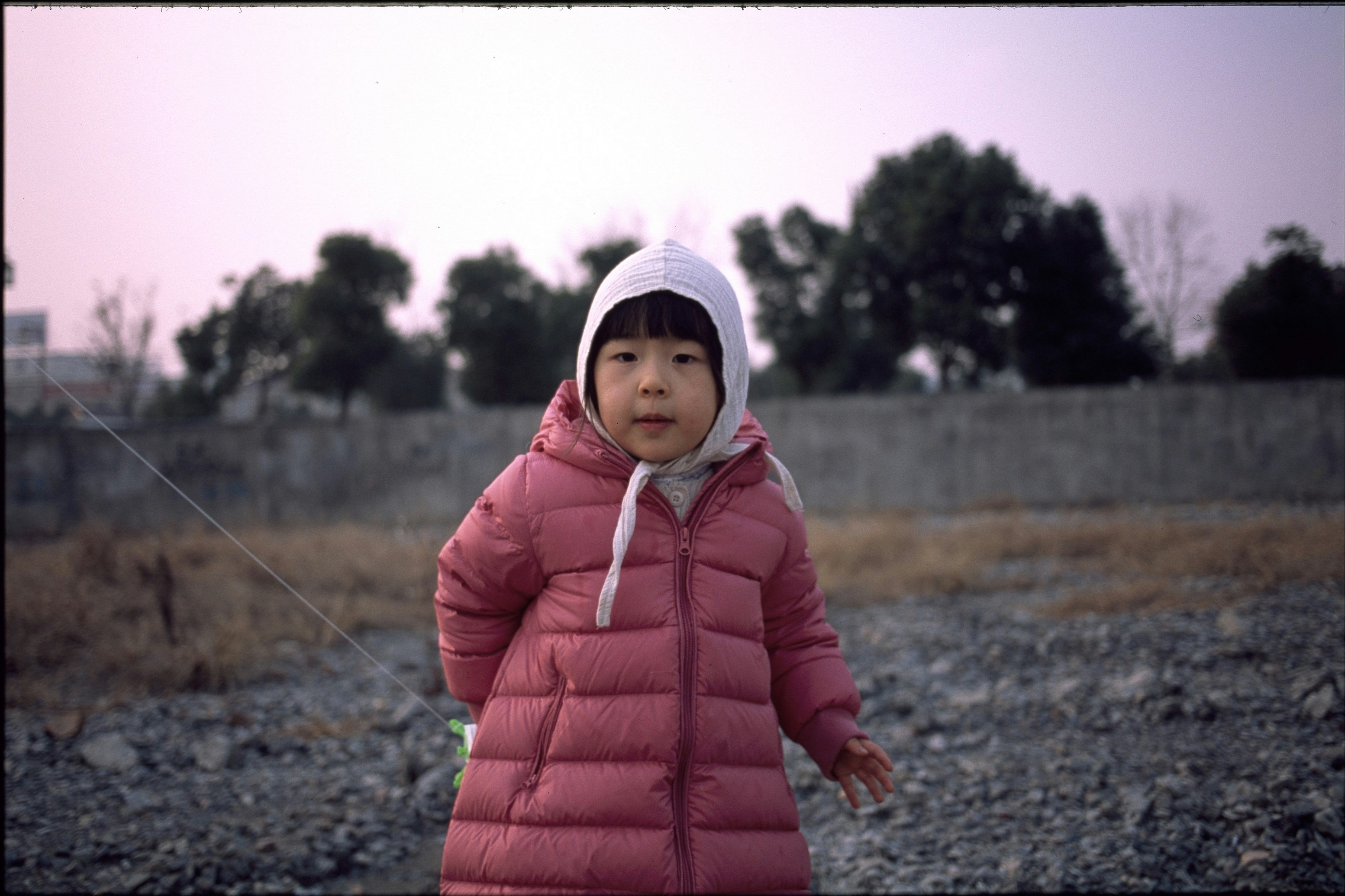 Girl in pink bubble jacket and white knit cap standing on gray concrete ...