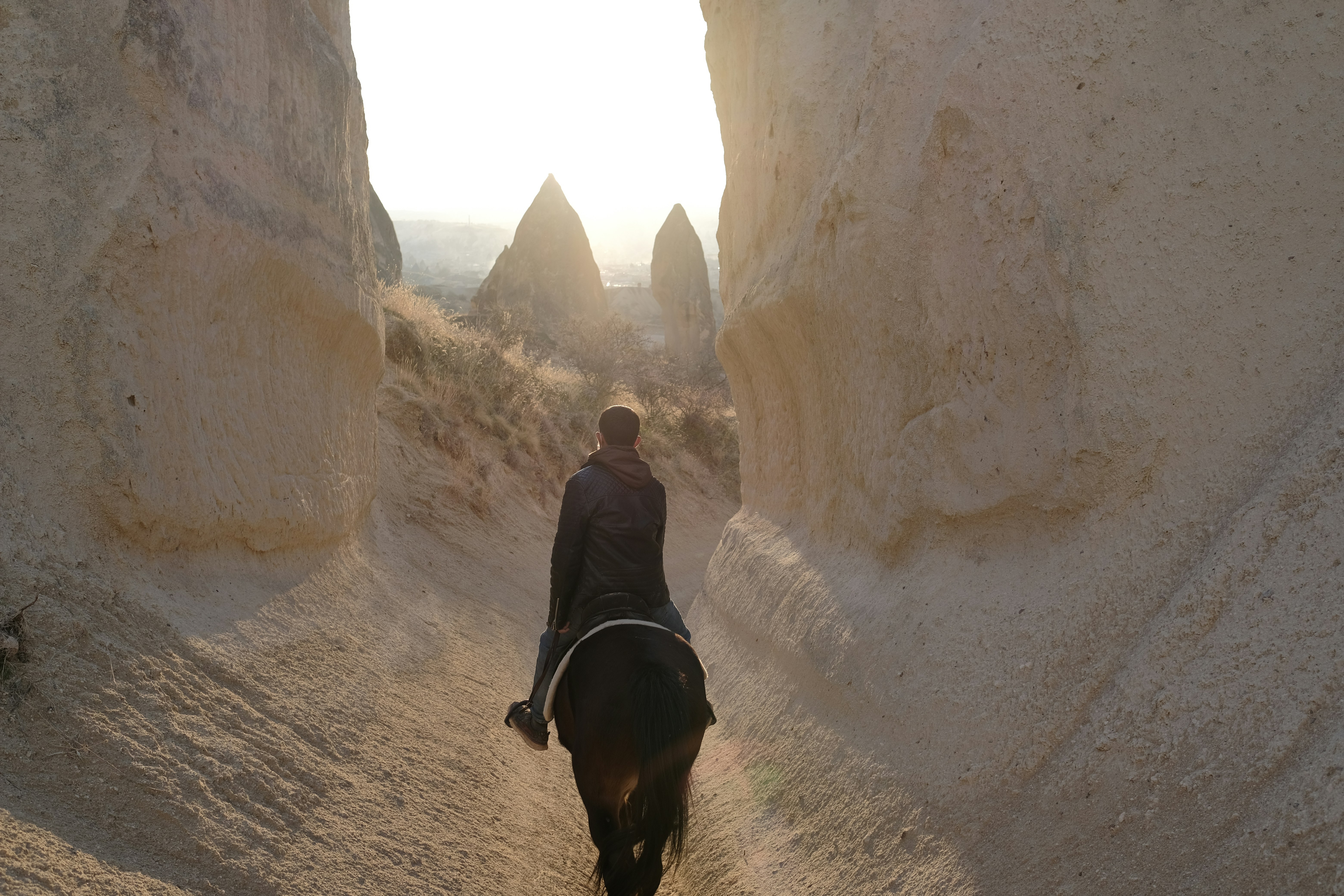 Rider on horseback traversing a narrow canyon with sunlight illuminating the distant rock formations.