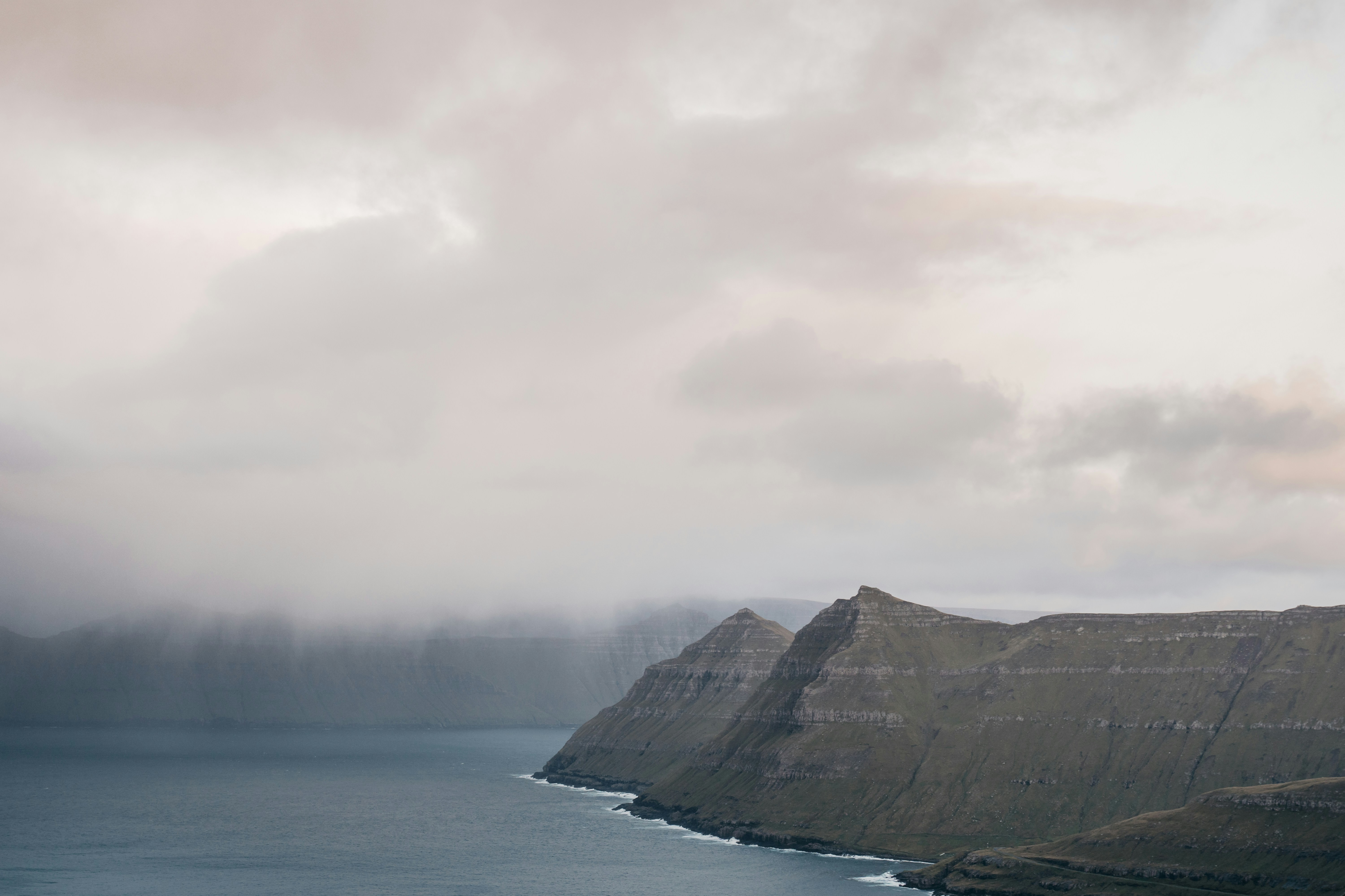 Dramatic cliffs meet the ocean under a blanket of clouds, capturing the raw beauty of the coastline. The scene evokes a sense of tranquility and nature's grandeur.