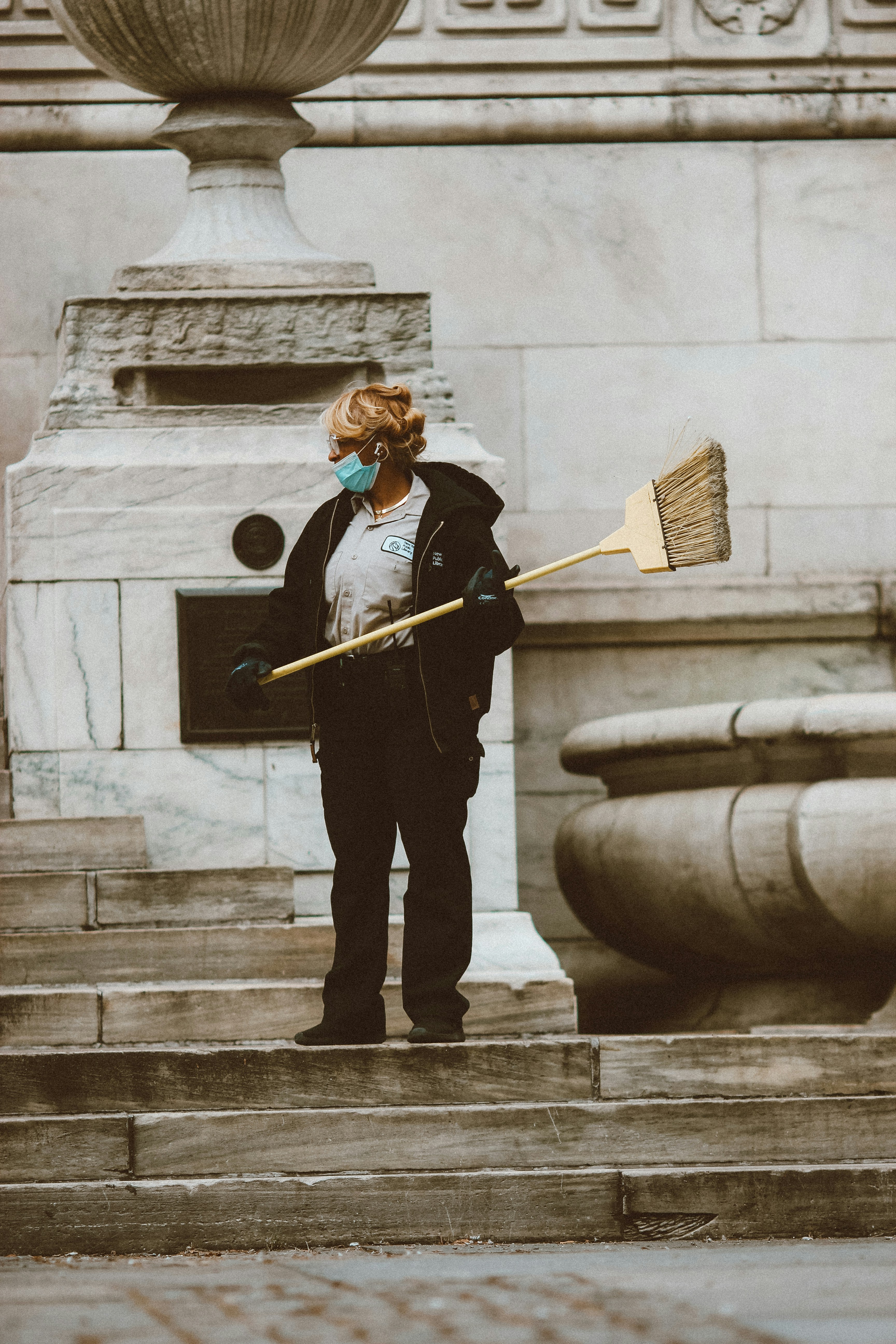 Masked Cleaner on Marble Steps: Broom in Hand Before a Grand Facade