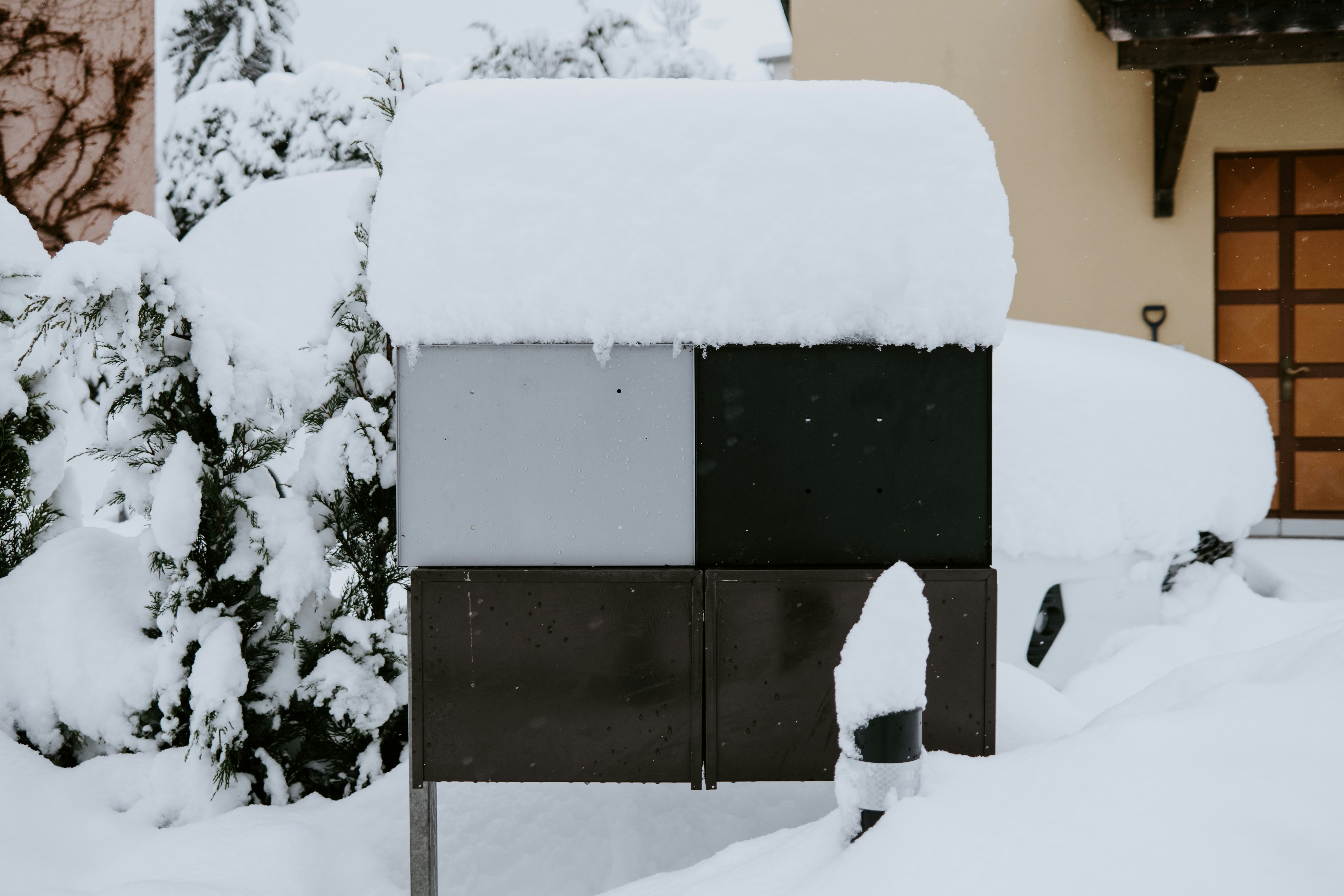 Mailbox partially buried under a thick layer of snow, showcasing a minimalist design with contrasting colors. The surrounding snow adds a serene winter atmosphere.
