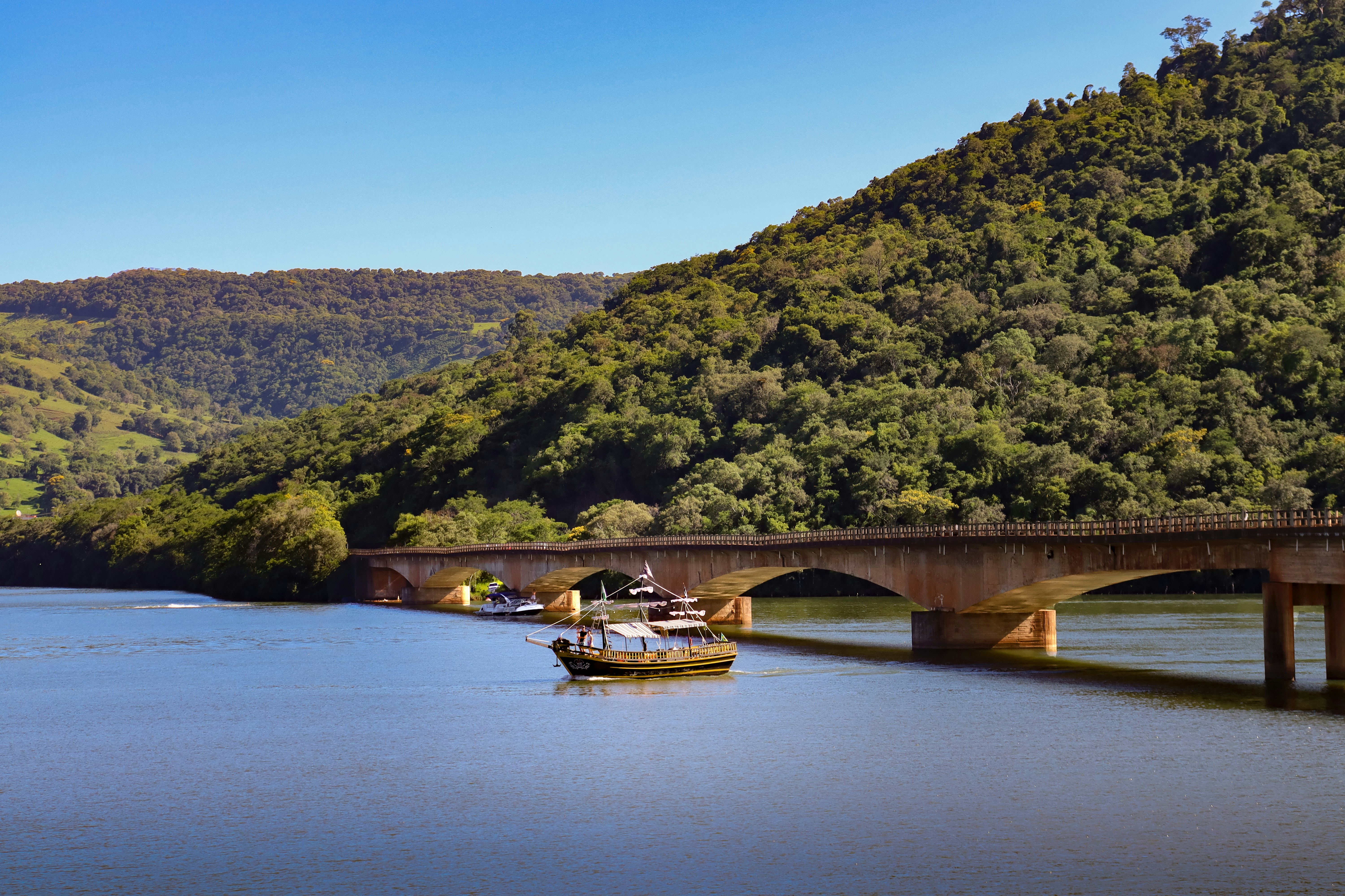 Boat anchored beneath a historic bridge with lush green hills in the background under a clear blue sky.