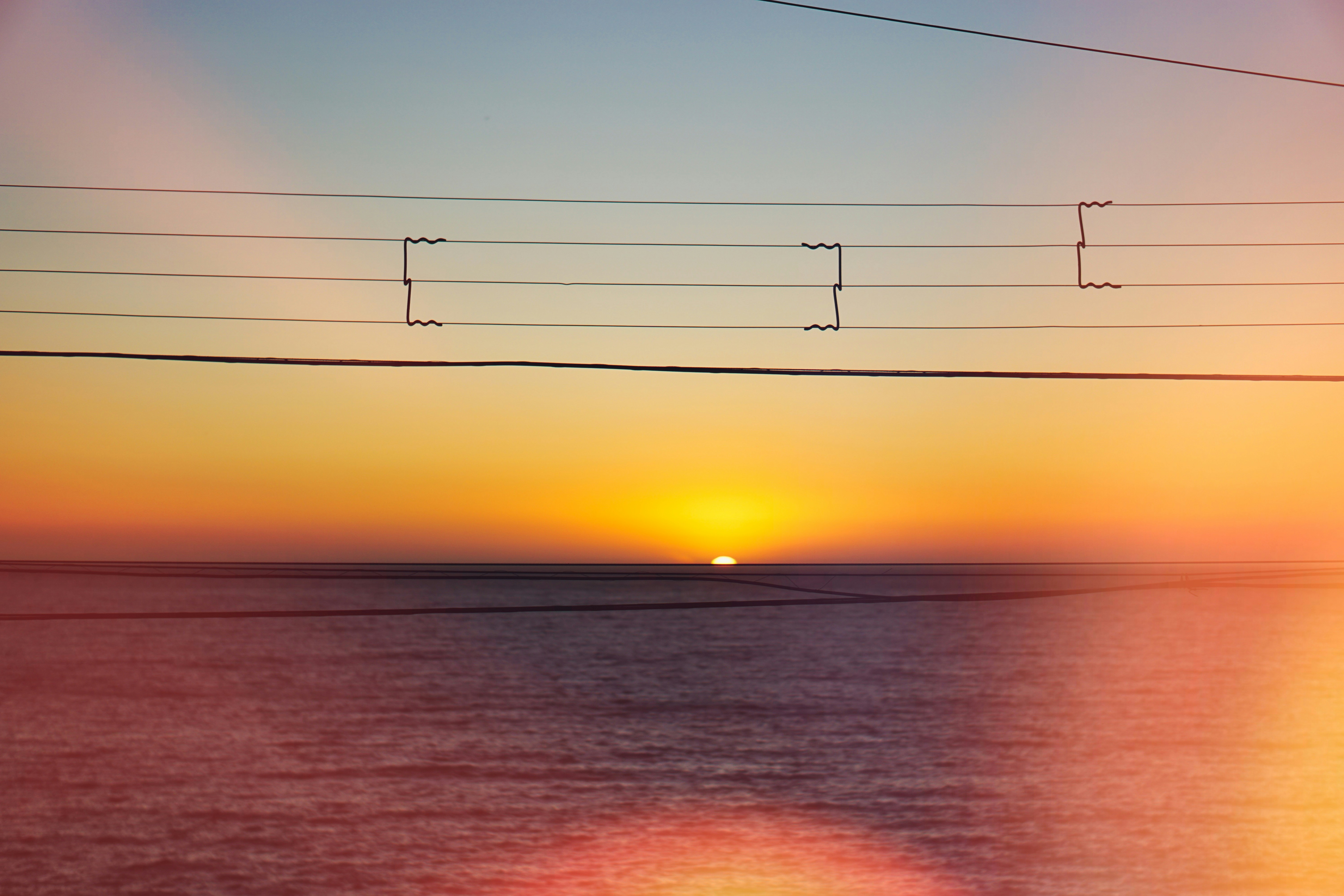 Vibrant sunset over the ocean, framed by silhouetted power lines against a gradient sky. 