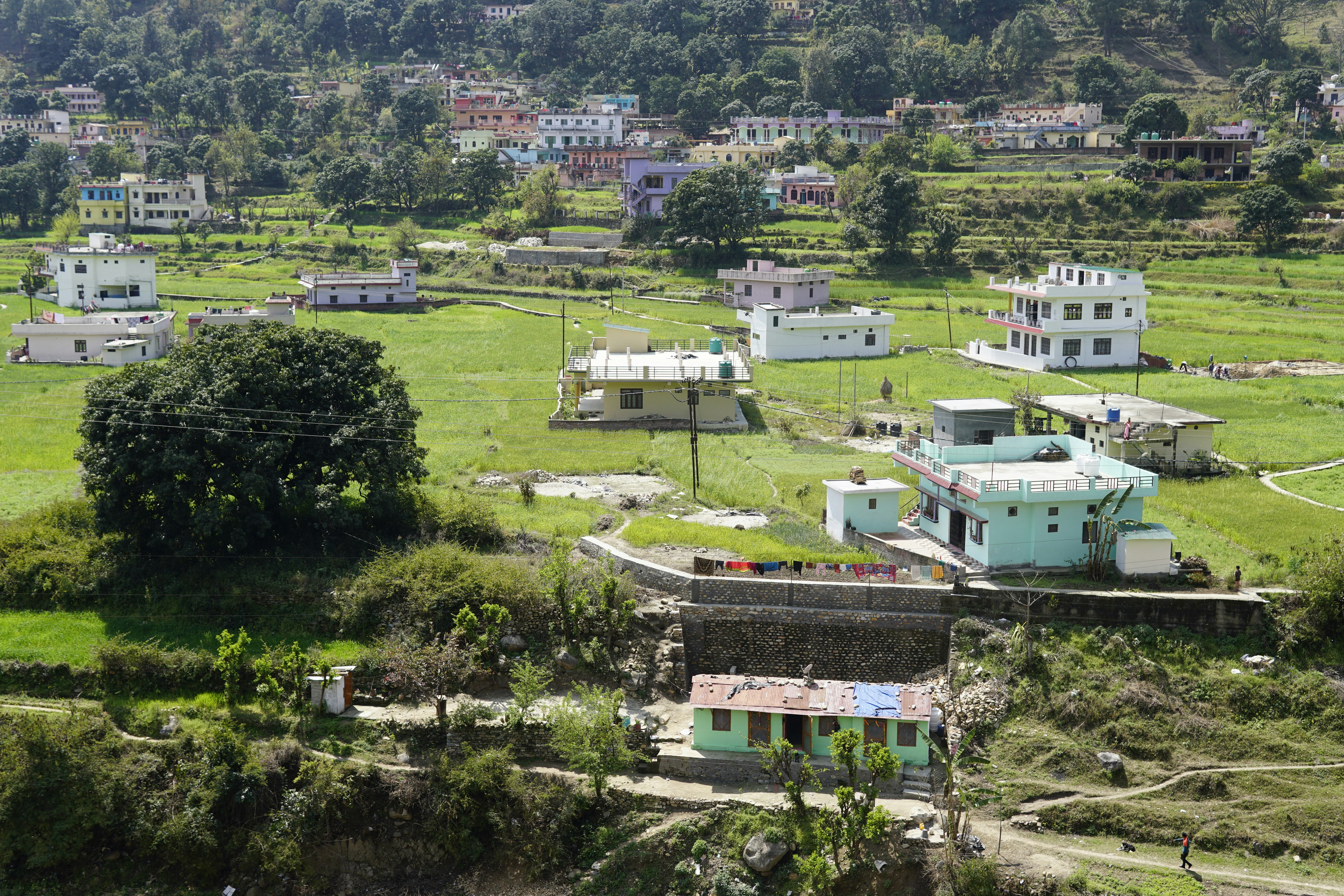 Scenic view of a rural settlement with colorful houses nestled among lush green fields and a backdrop of hills.