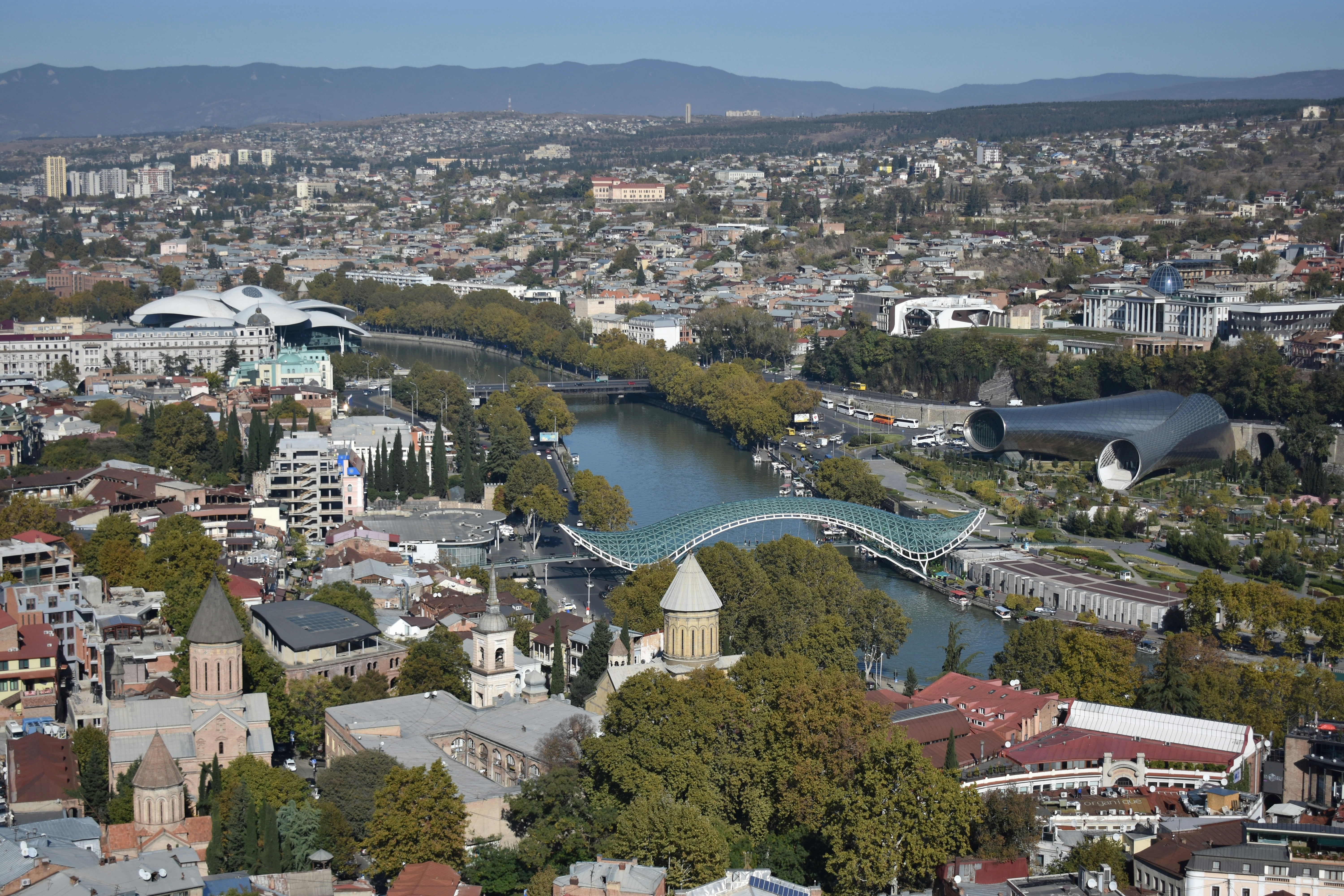 Cityscape featuring a modern pedestrian bridge over a winding river, surrounded by a blend of historic and contemporary architecture.