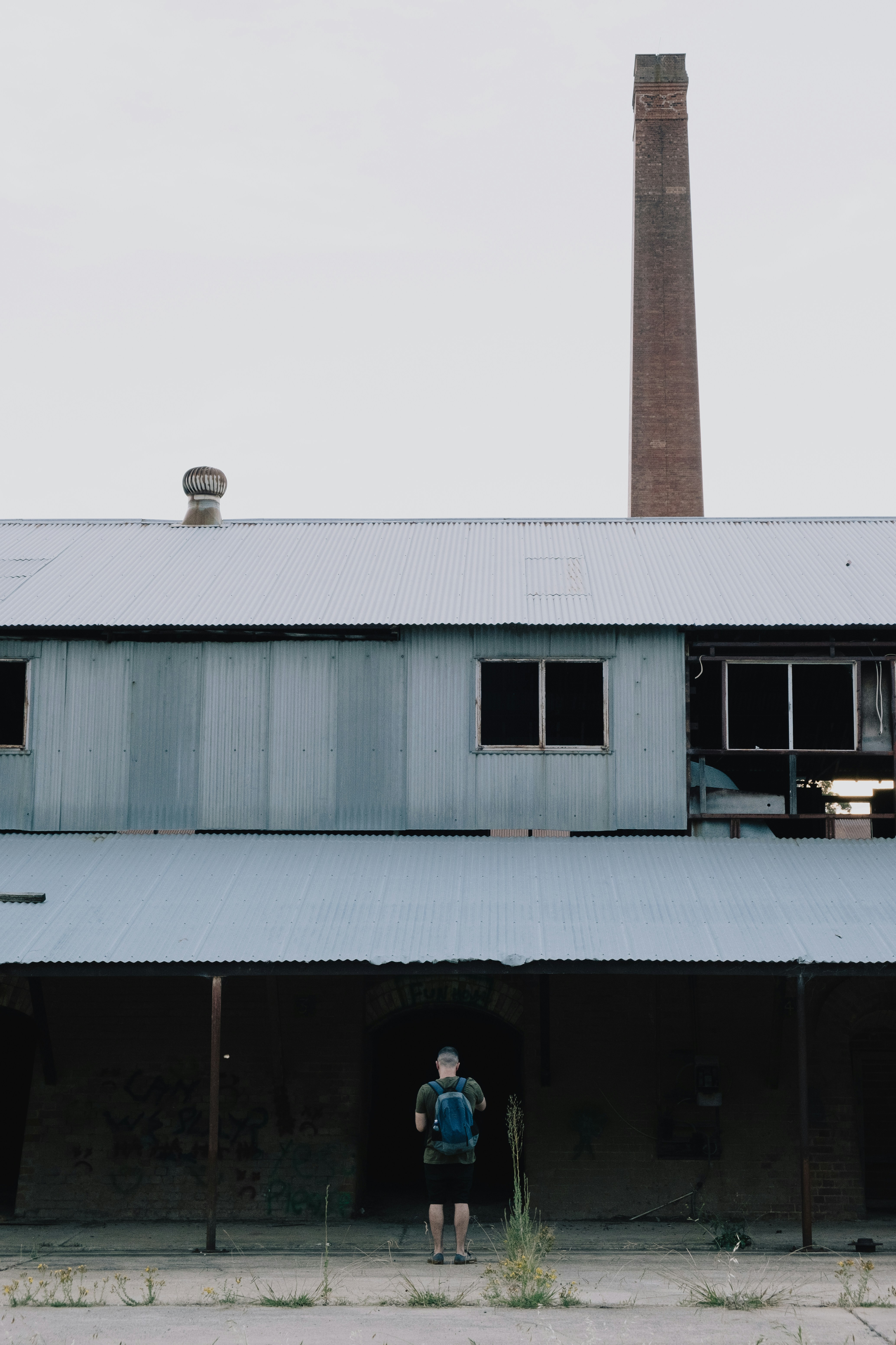 Lone Backpacker at the Threshold of a Weathered Factory