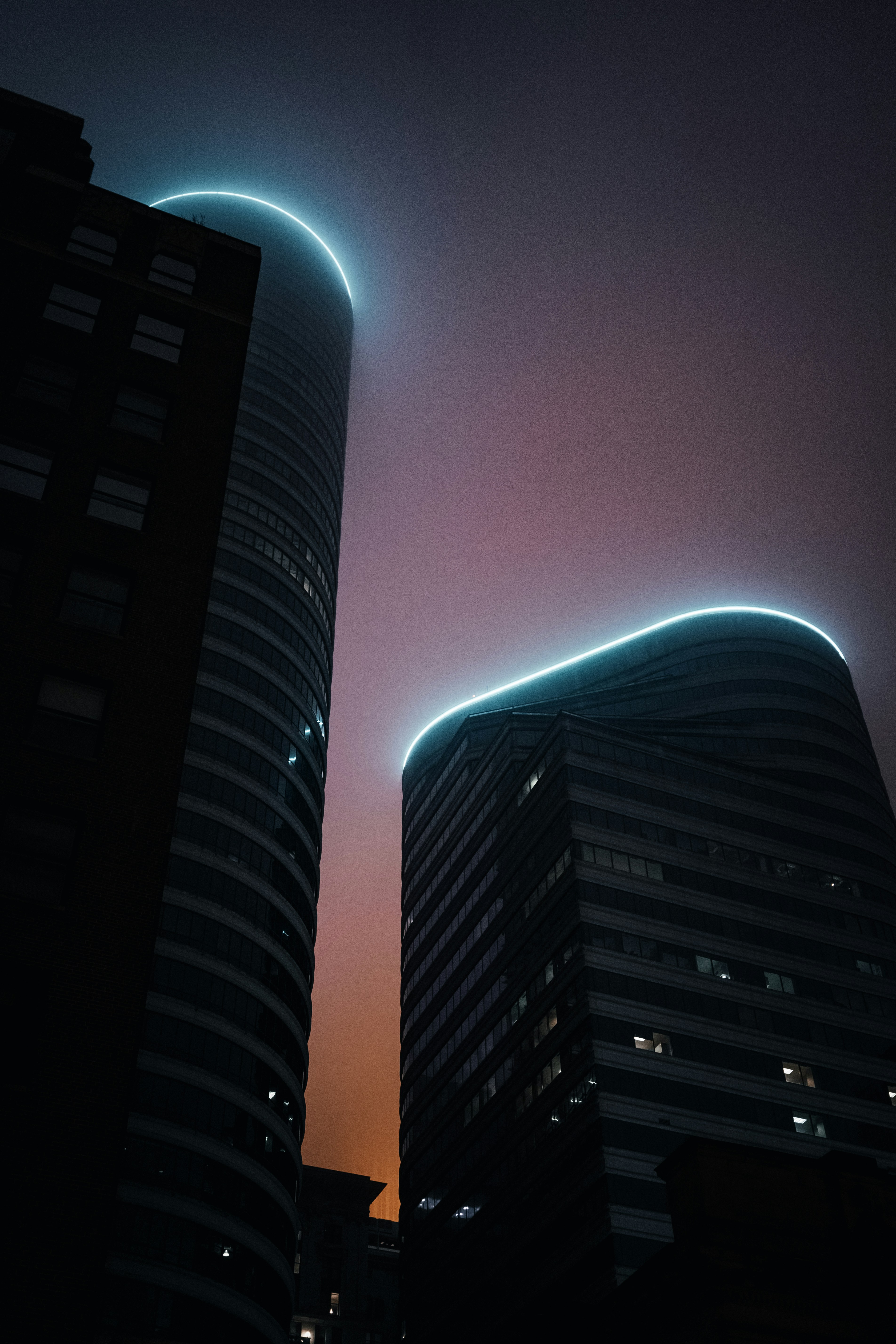 Two modern skyscrapers with glowing edges pierce the foggy twilight, creating a striking silhouette against a gradient sky.
