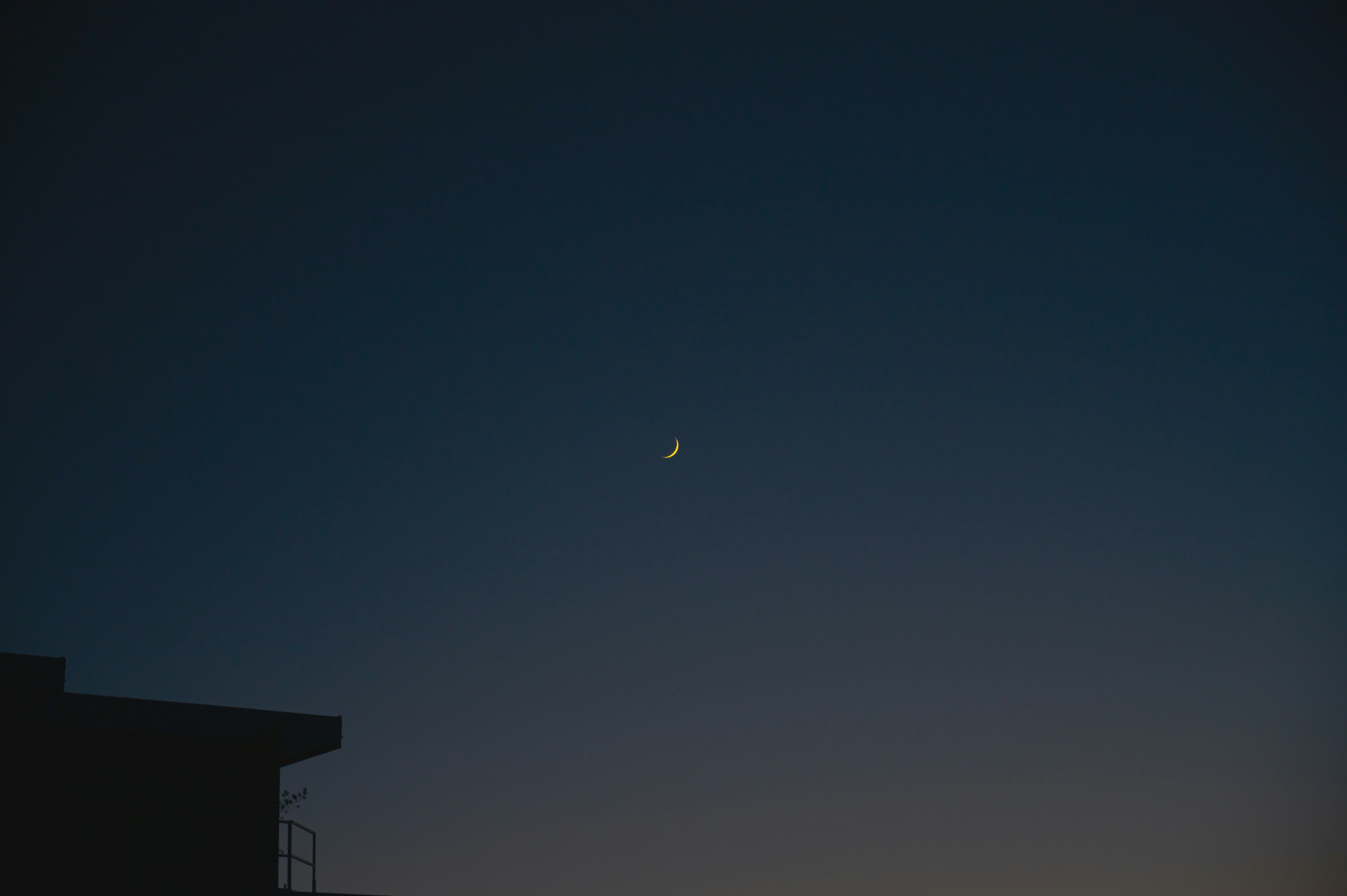 Crescent moon hangs delicately in the twilight sky, framed by a silhouetted building. The serene transition from day to night is captured beautifully.