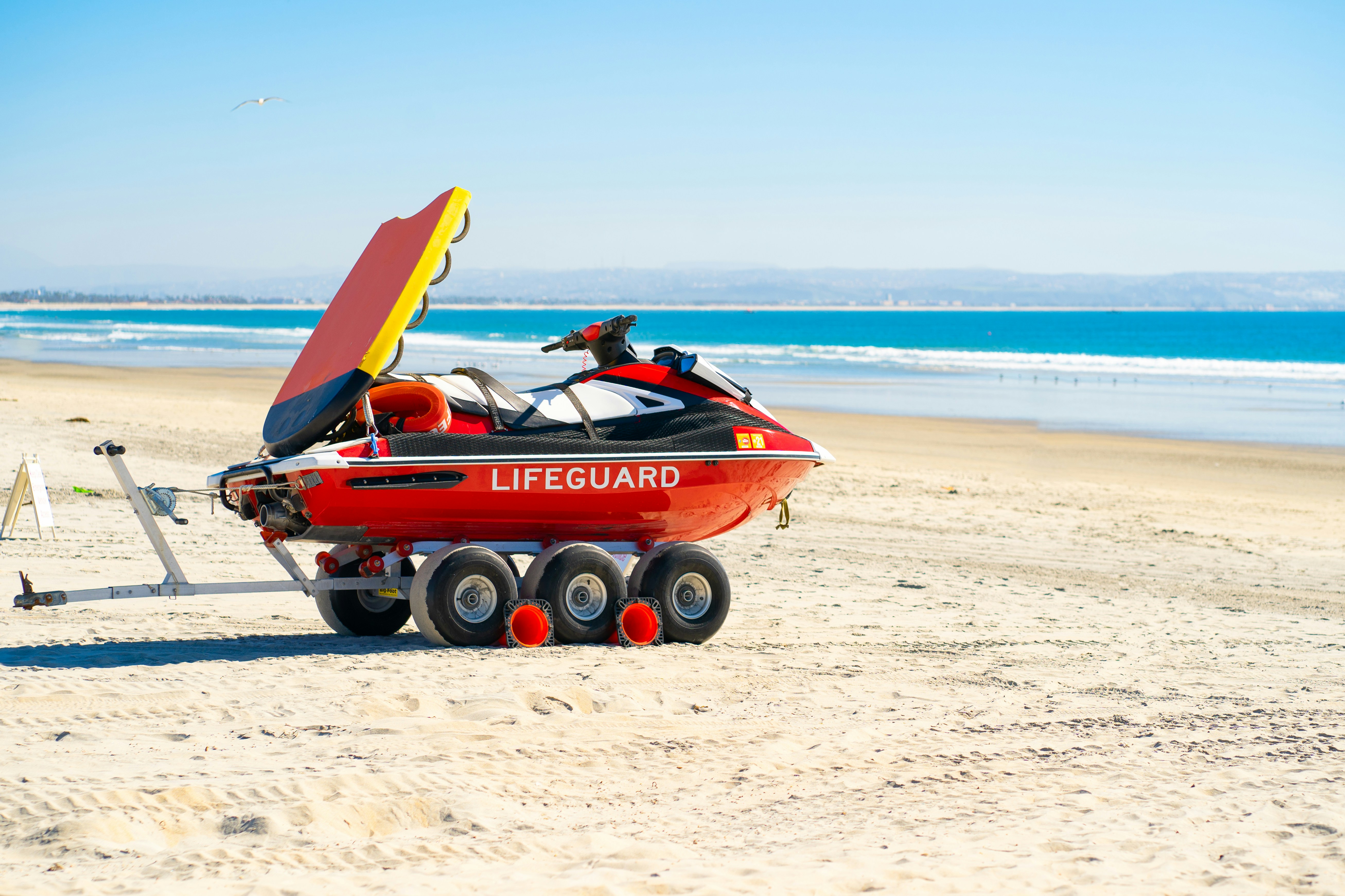 Lifeguard jet ski parked on the sandy beach, with the ocean stretching out in the background. The bright colors of the jet ski contrast with the serene blue waters.