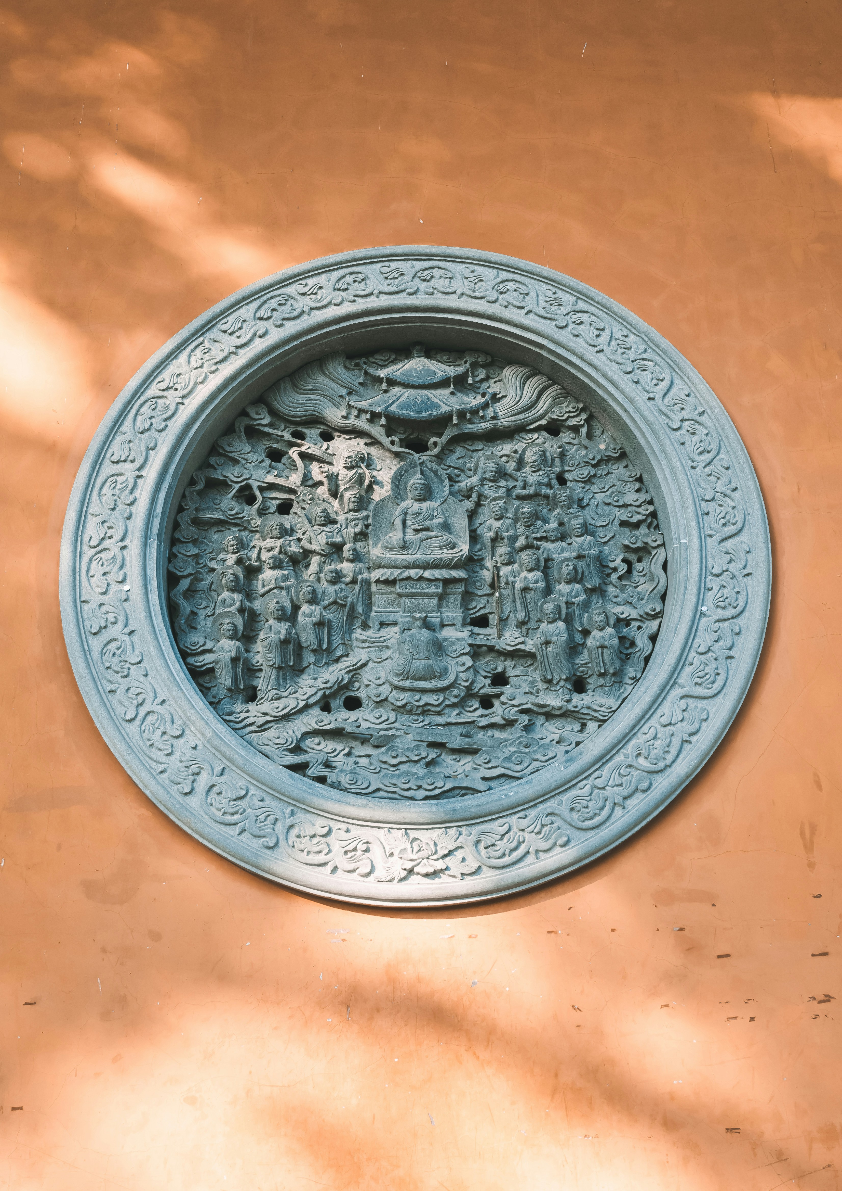 Intricate stone relief depicting a serene Buddha surrounded by figures, set against a warm, earthy background.