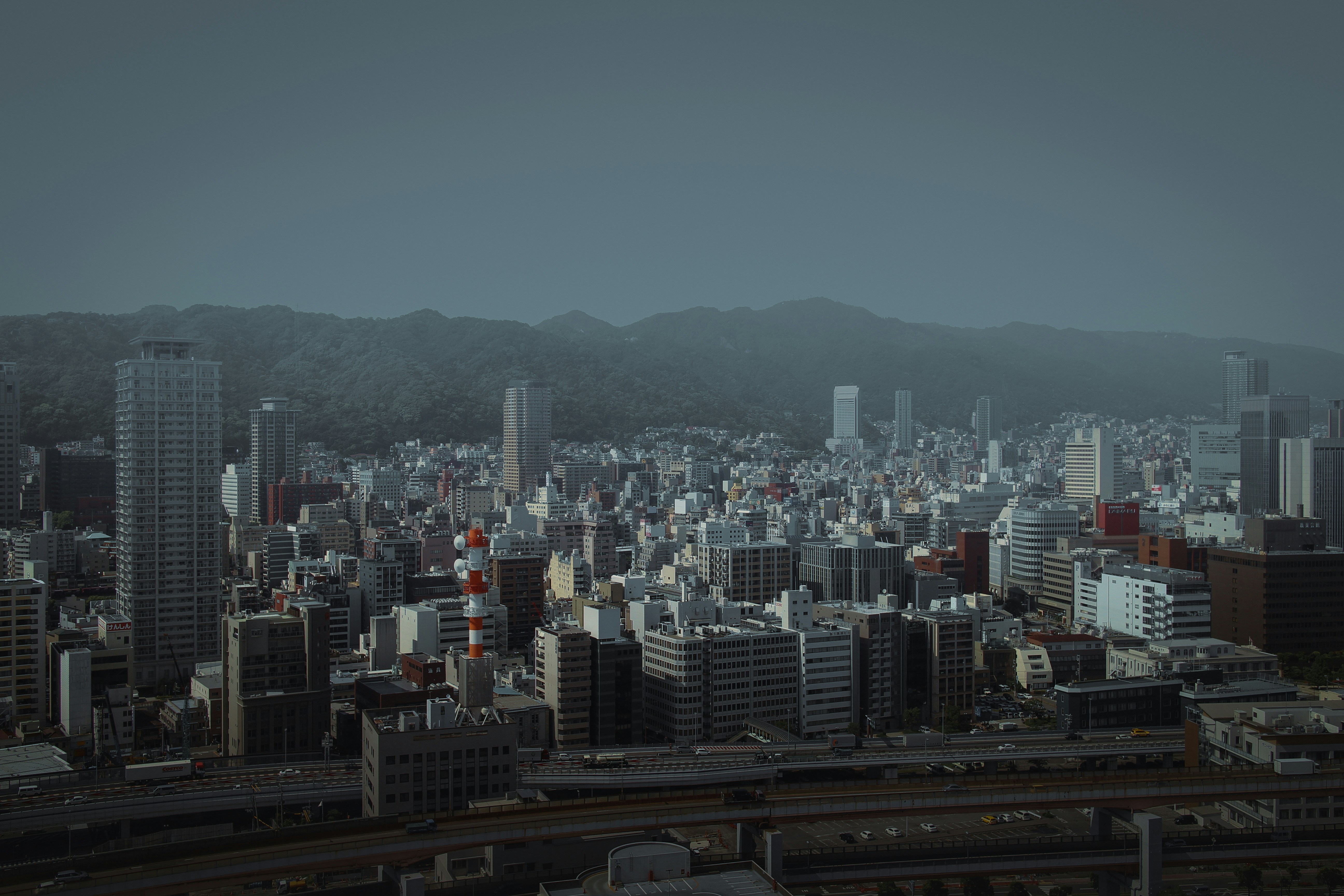 City skyline with towering buildings against a backdrop of distant mountains under a clear blue sky.