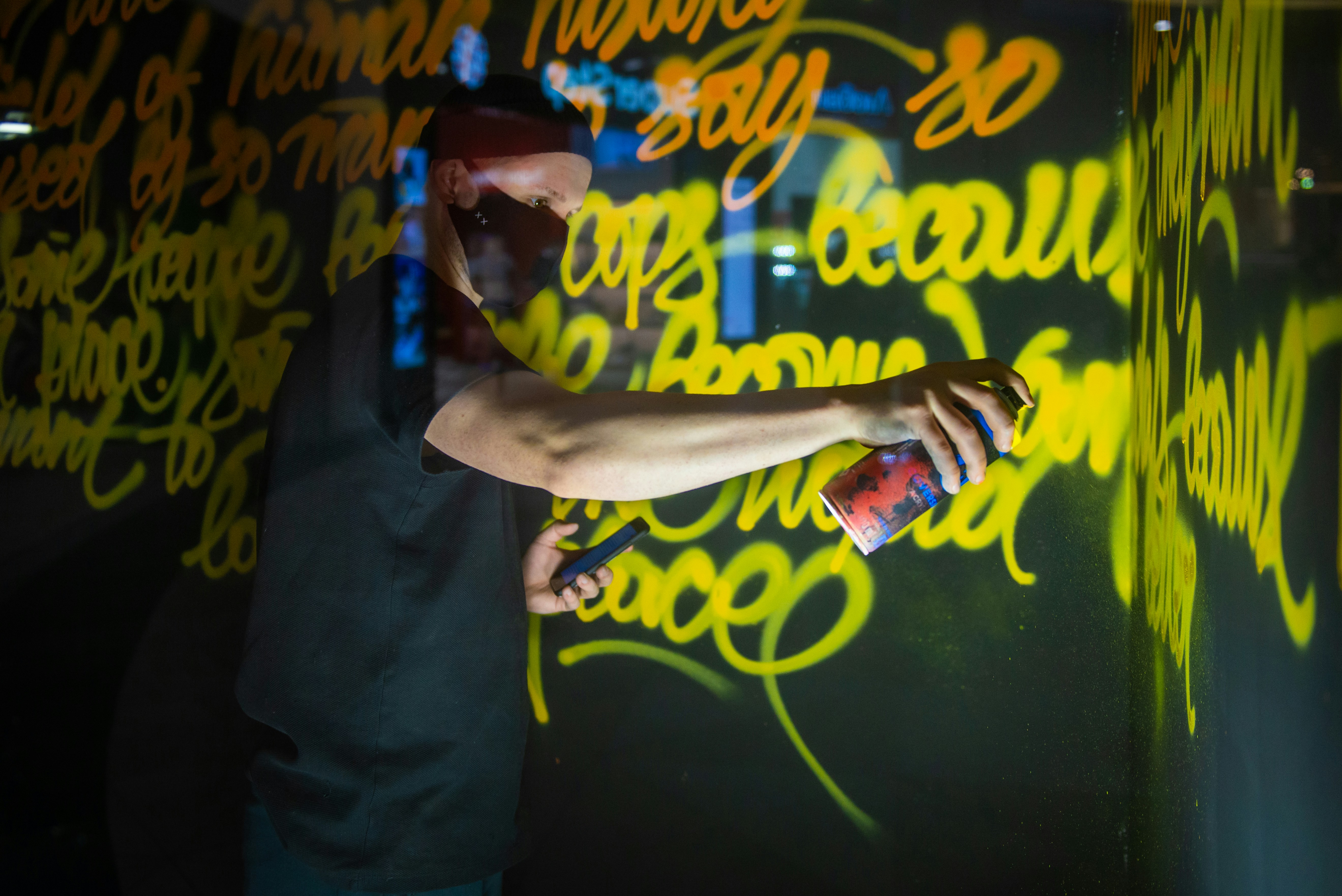 Neon Script in Motion: A Spray Painter Traces Yellow Graffiti Across a Shadowed Wall