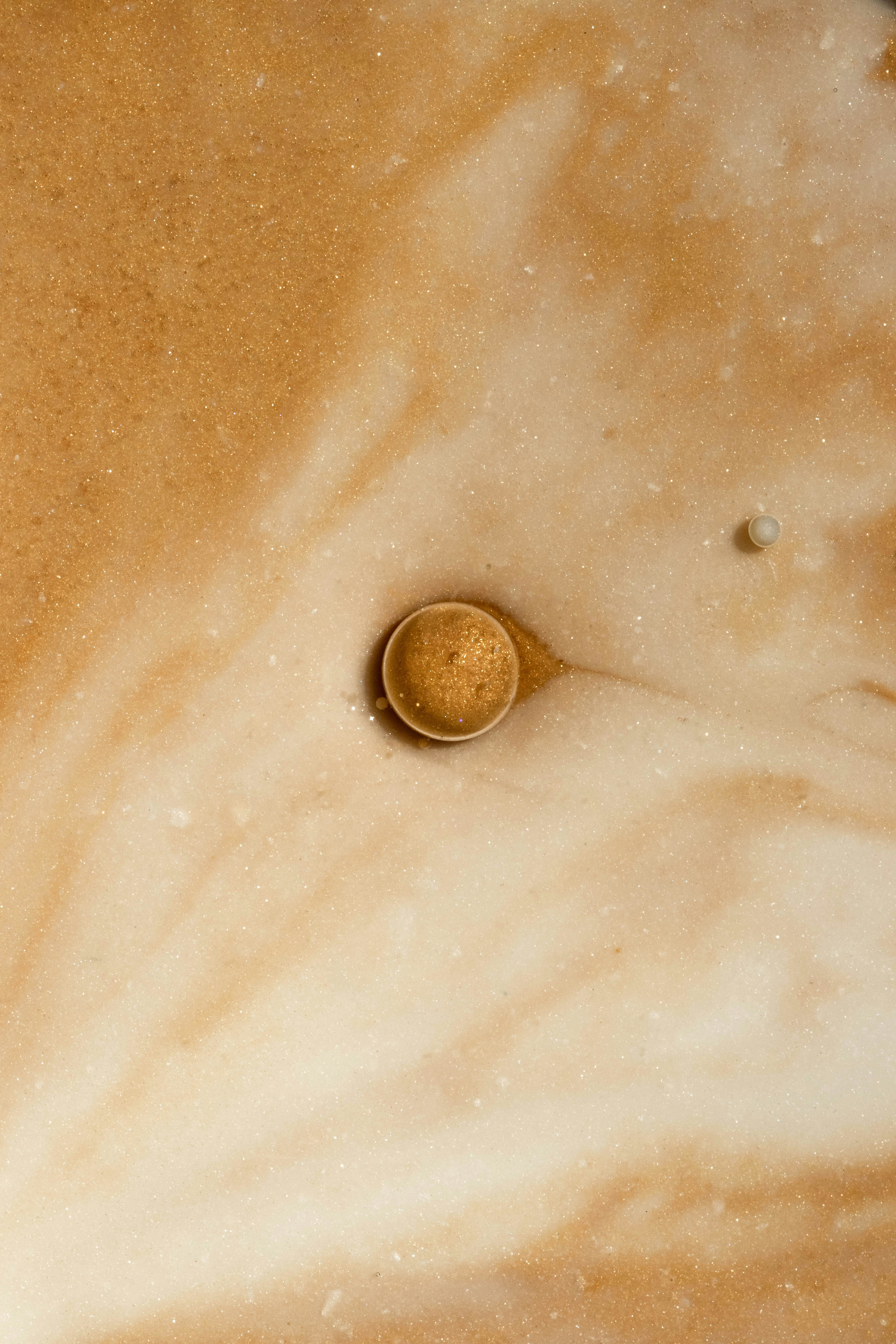 A golden sphere nestled in a swirl of sandy textures, reflecting light and creating a sense of depth. The subtle interplay of colors enhances the visual intrigue.