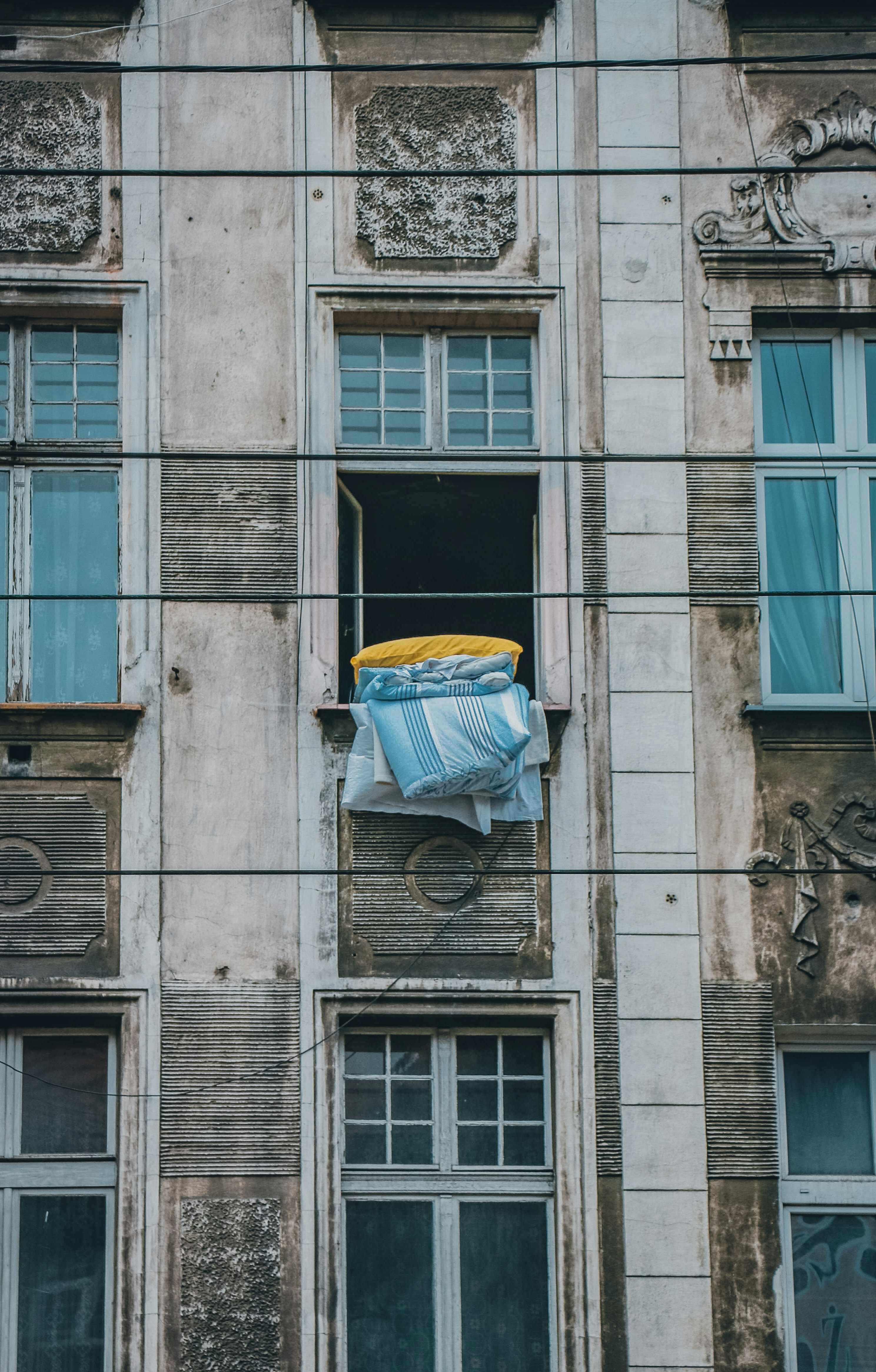 Open Window, Bright Bedding: A Quiet Burst on a Worn City Facade