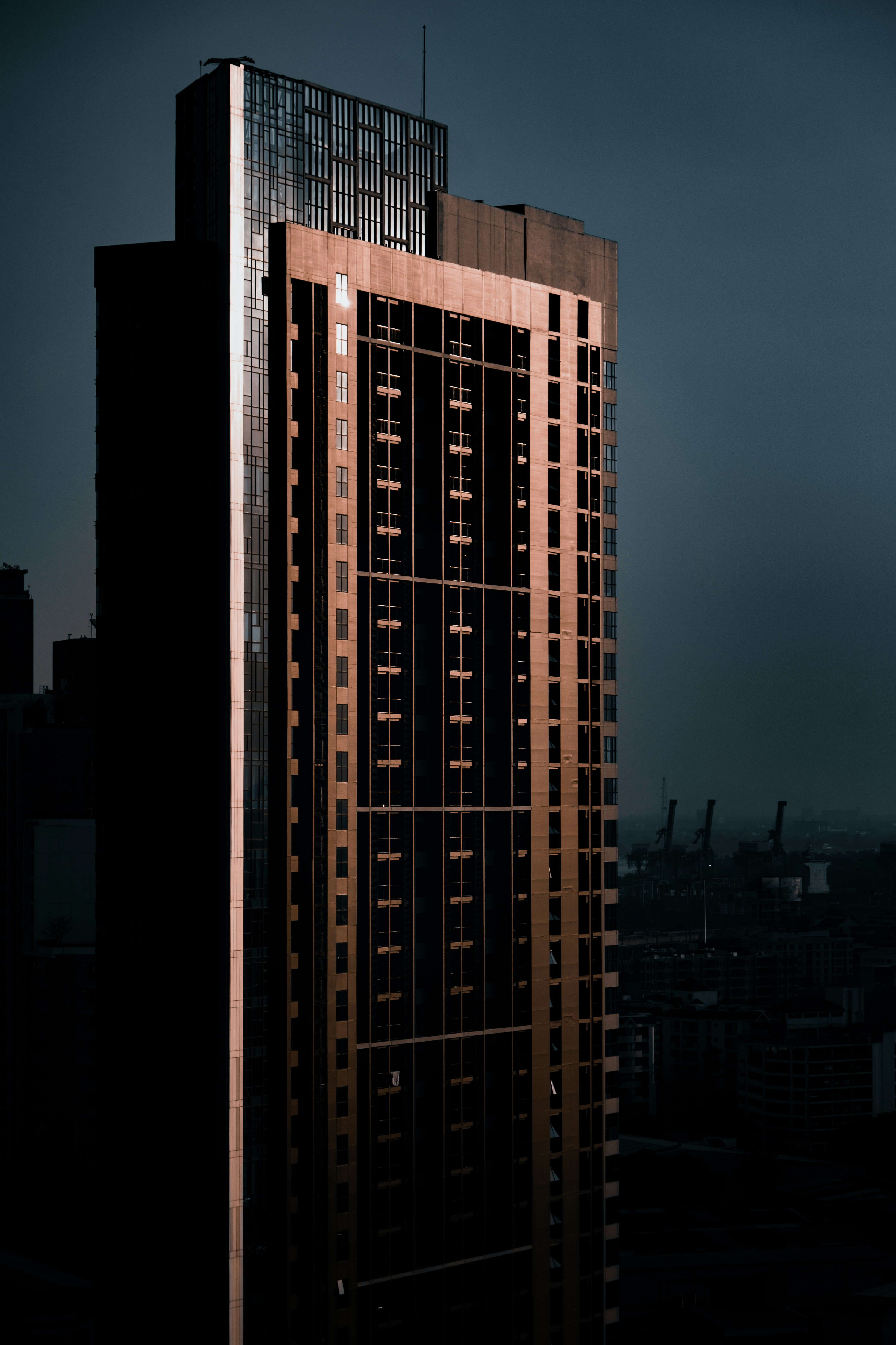 Tall modern skyscraper illuminated by soft light against a dark sky, showcasing architectural lines and textures.