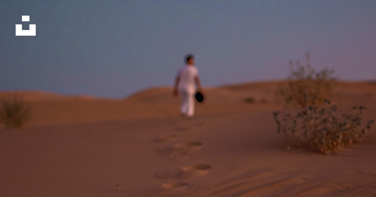 Person In White Shirt Walking On Brown Sand During Daytime Photo Free