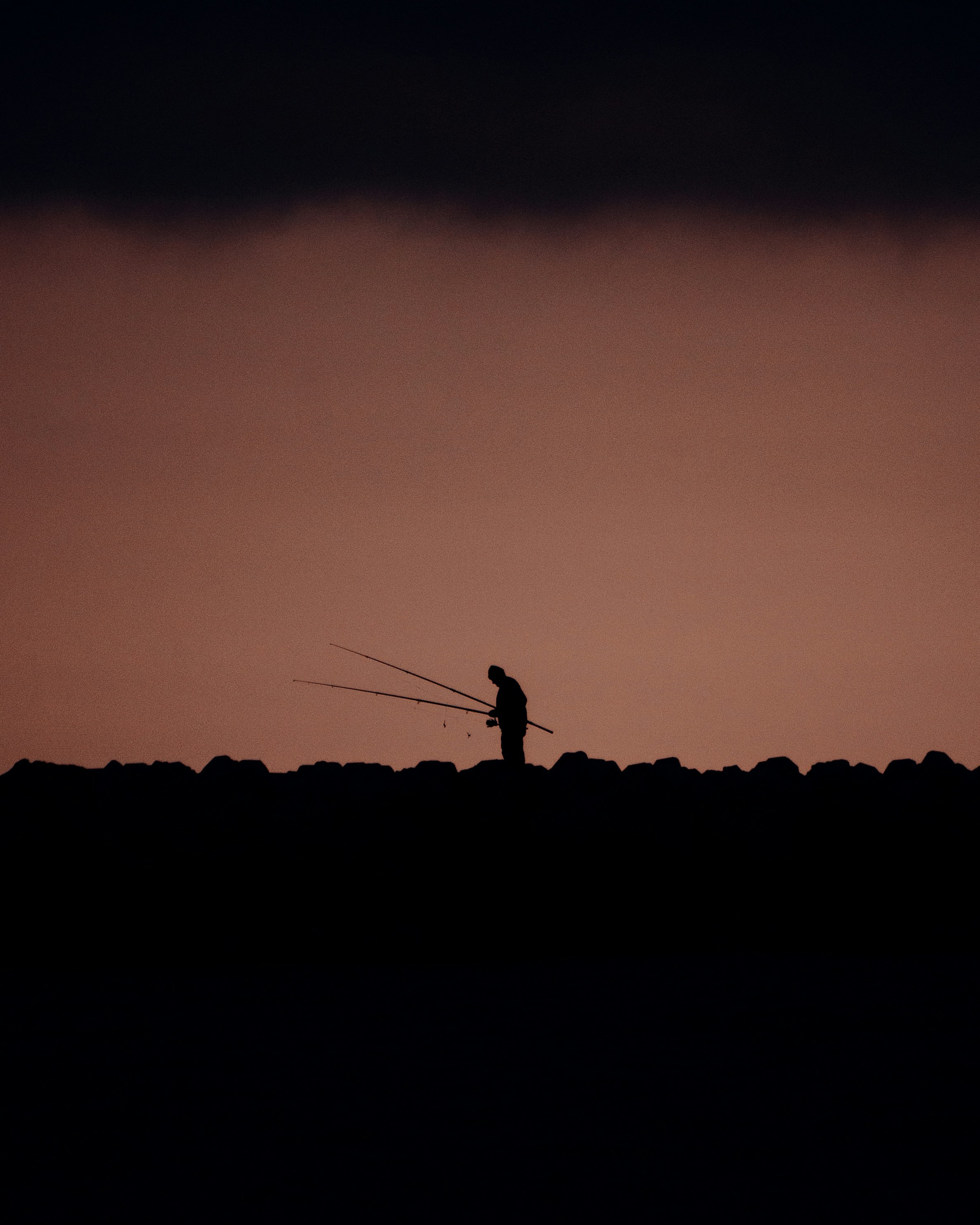 Twilight Angler: silhouette on a rocky shore with multiple fishing rods