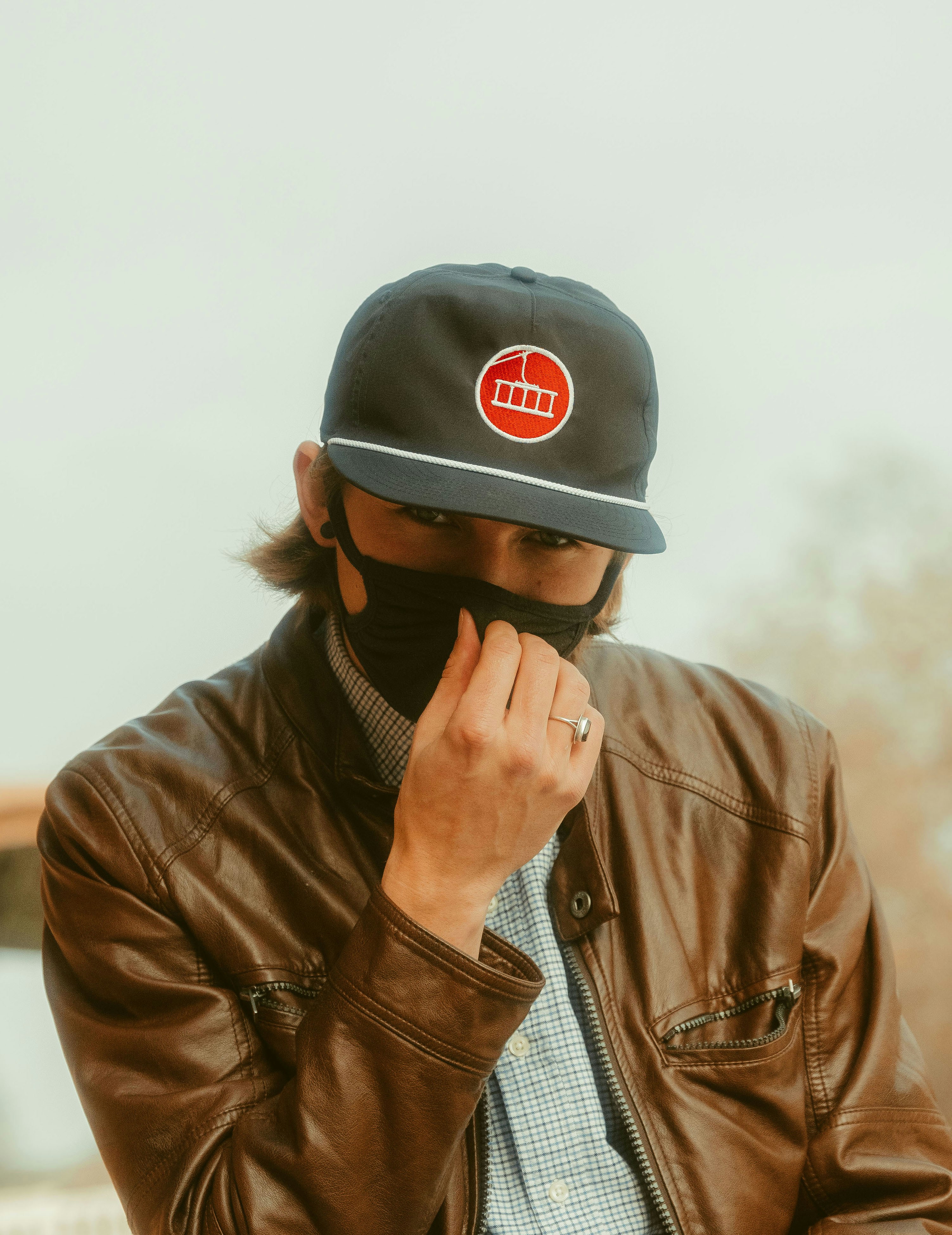 Man in brown leather jacket wearing black fitted cap covering his face ...