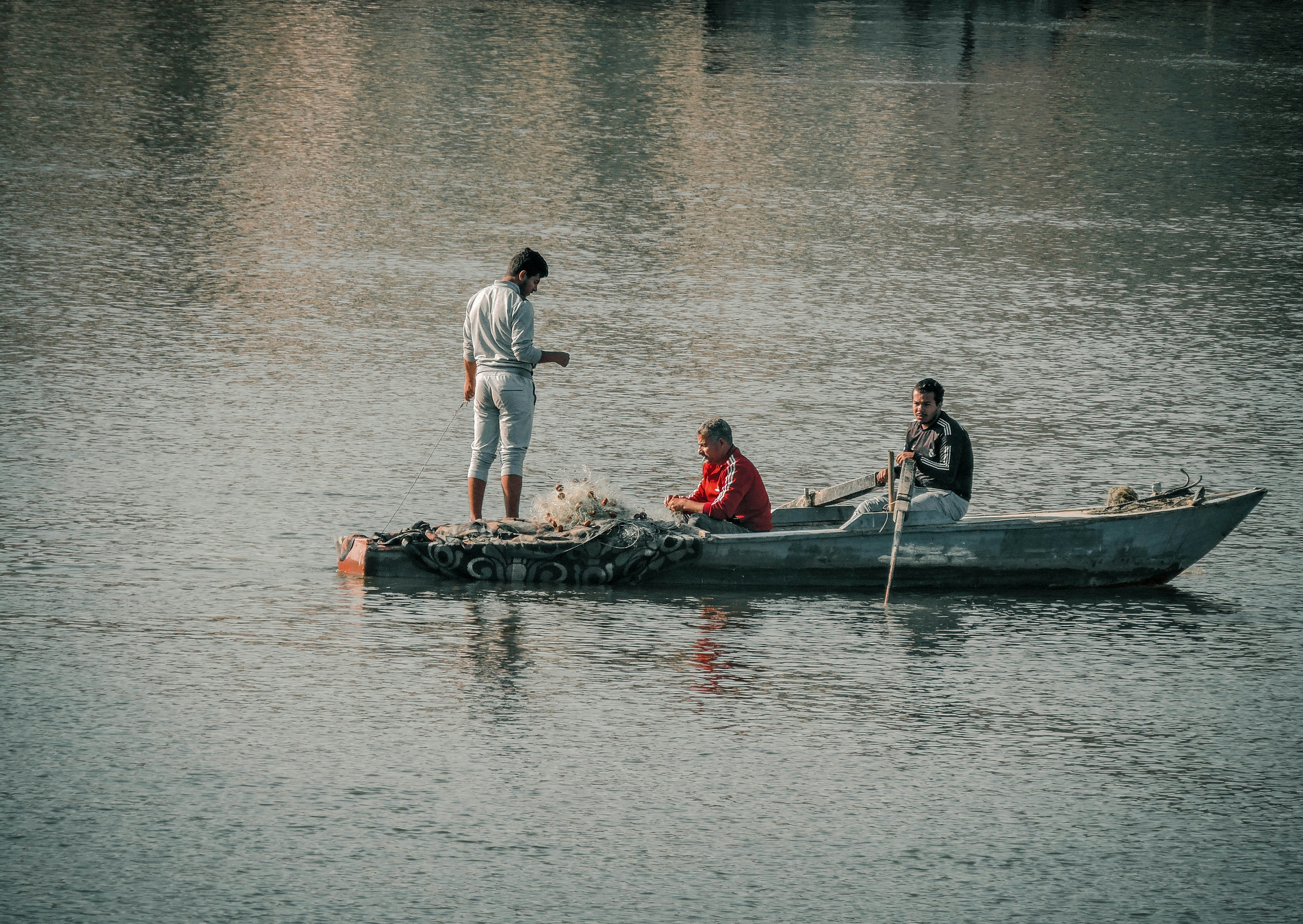 Three fishermen on a small boat casting nets in tranquil waters, showcasing the essence of traditional fishing life.