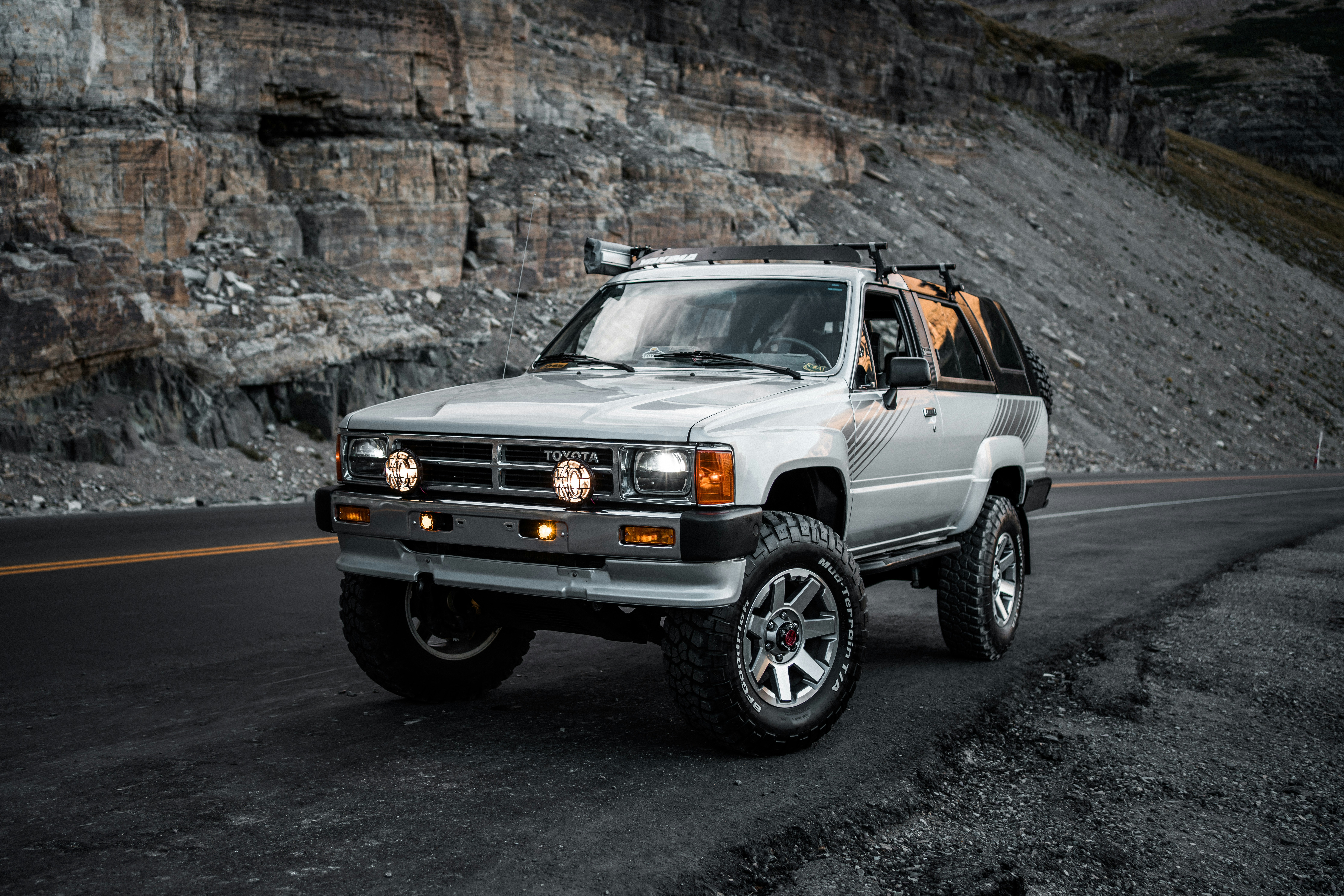 Silver Toyota 4Runner parked on a winding mountain road with rugged cliffs in the background.