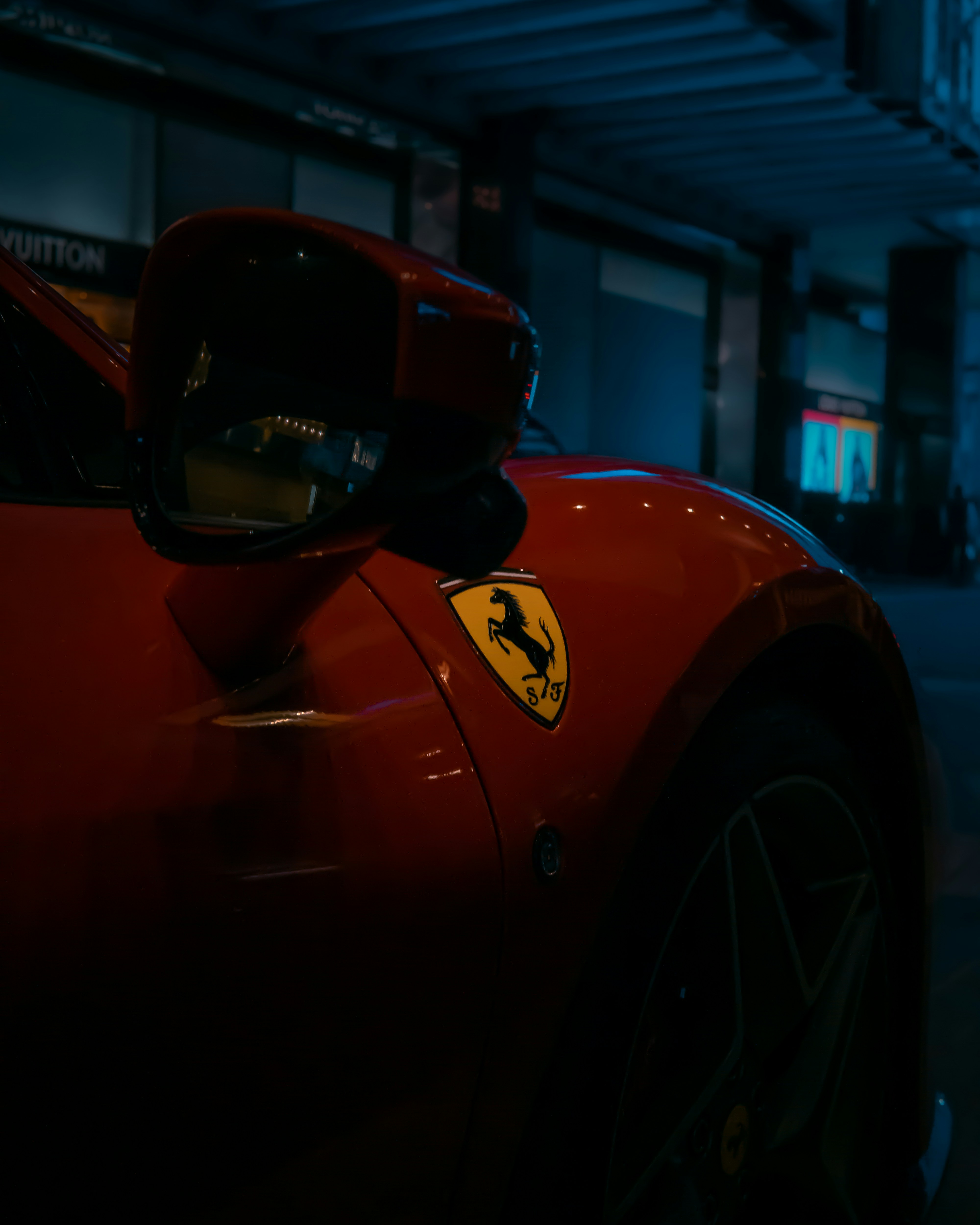Close-up of a Ferrari's emblem and side mirror, showcasing its sleek design against a moody urban backdrop.