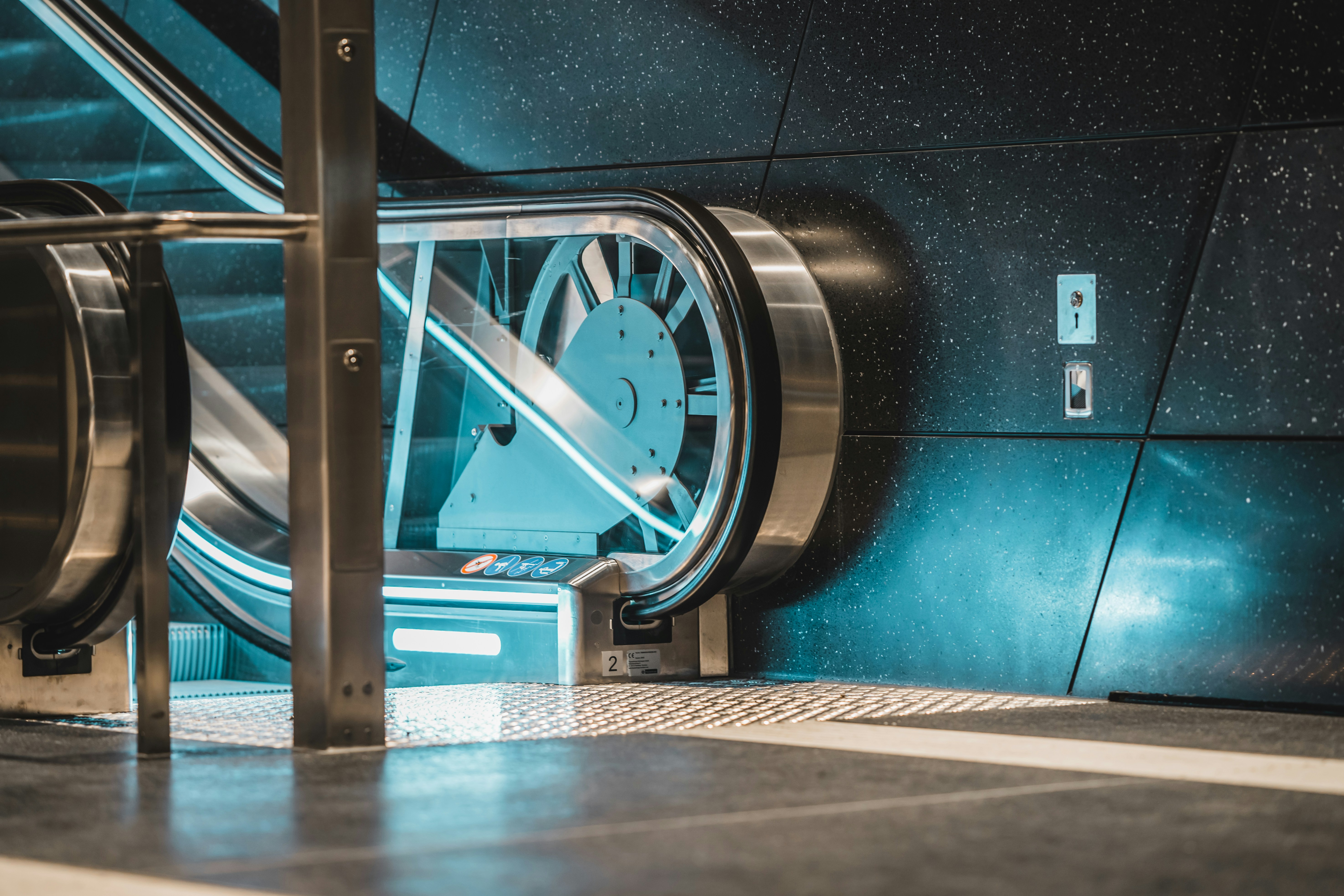 Close-up of an escalator mechanism with sleek metallic elements and a cool blue light.