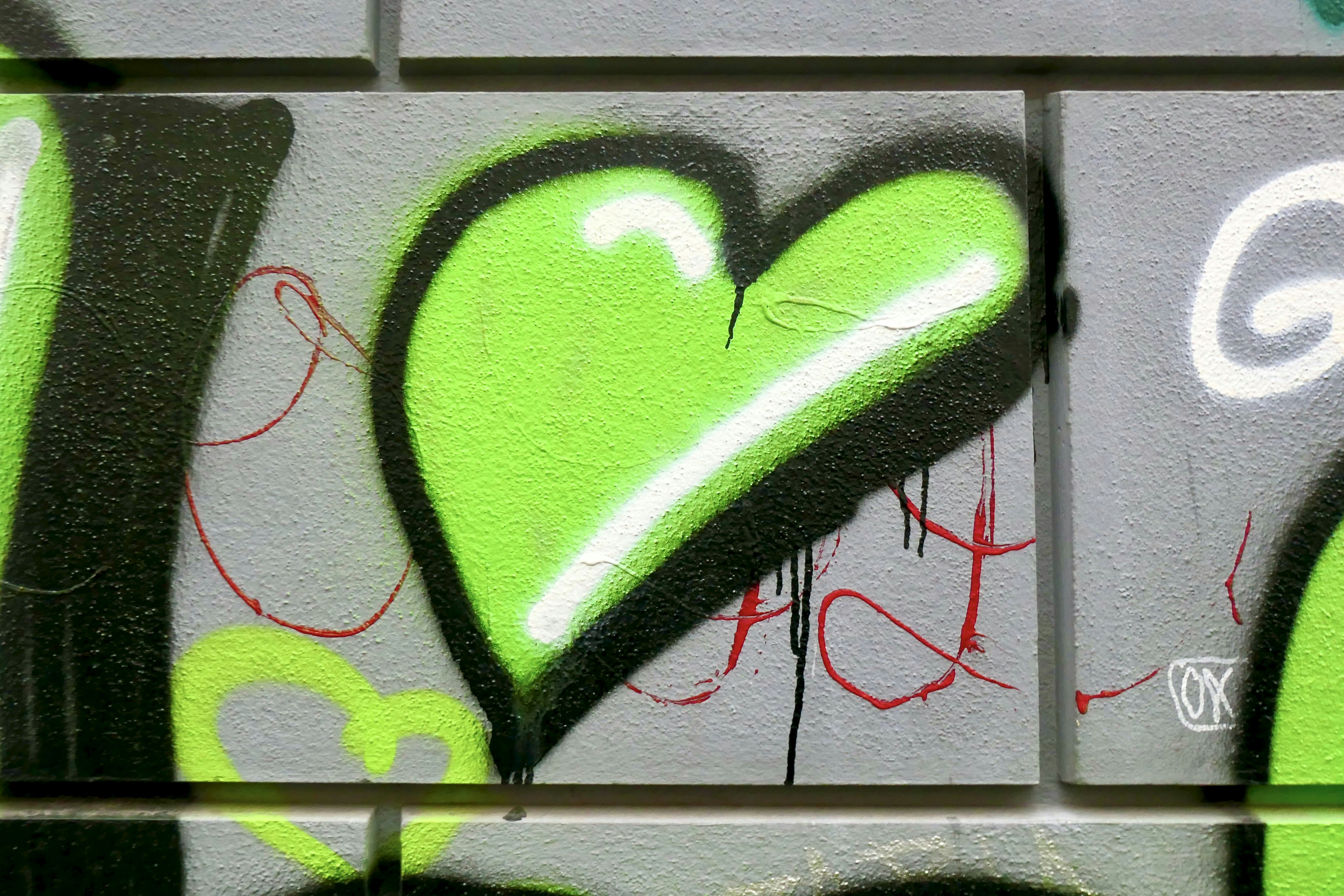 Bright green heart graffiti with black outline on a textured wall, accented by red and black spray paint drips.