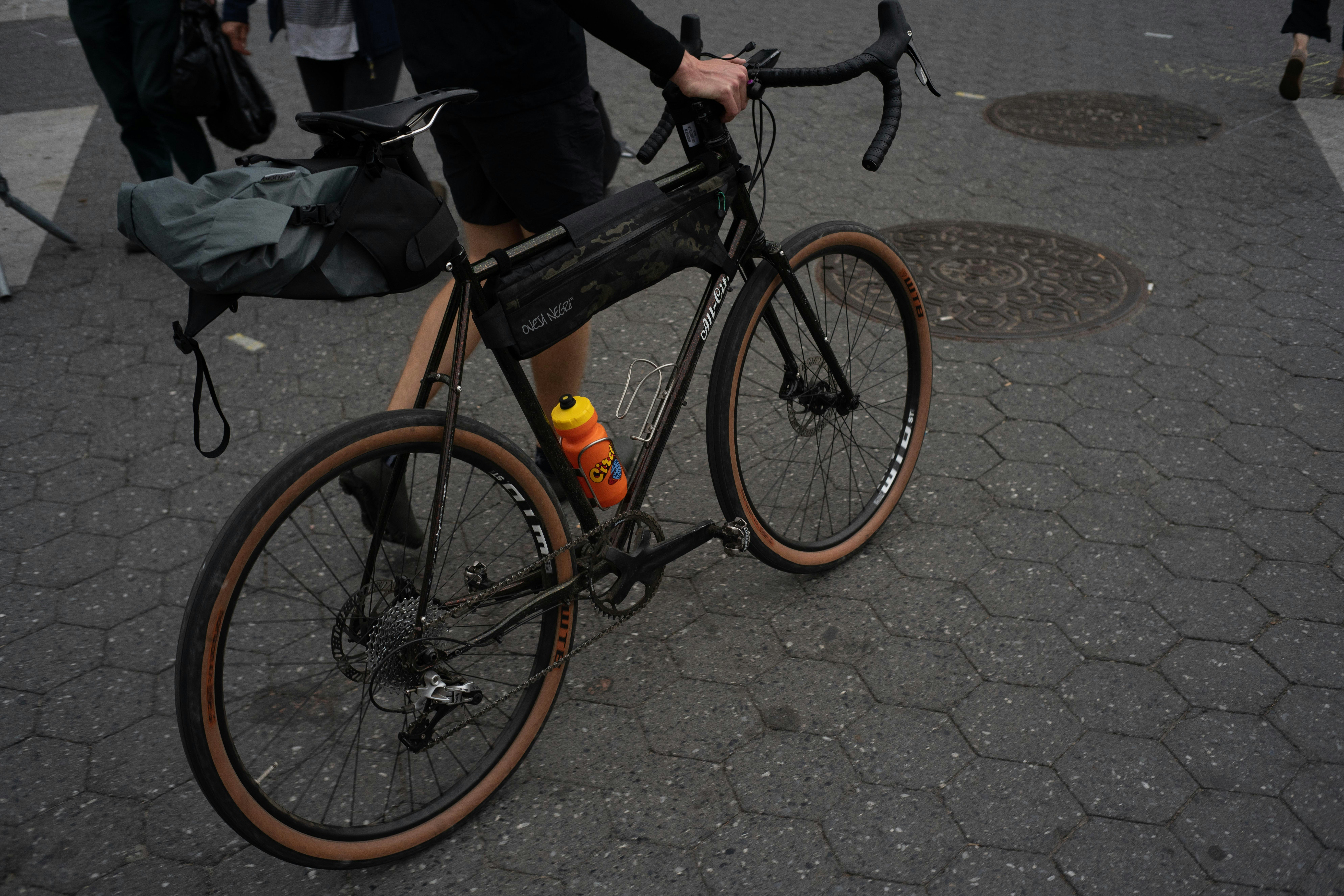 Cyclist standing with a black bike on a textured city pavement.