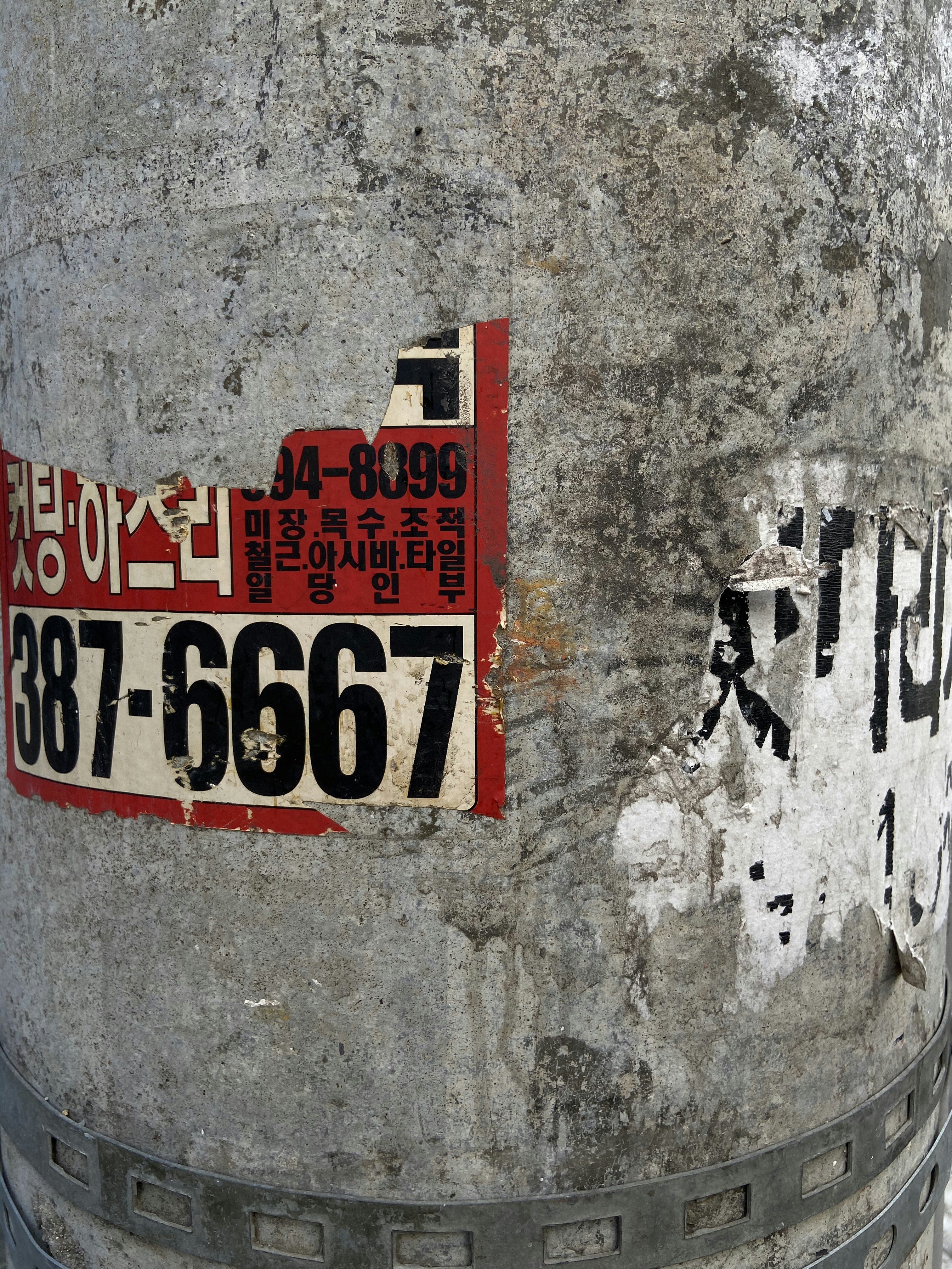 Weathered utility pole with bold red and black posters peeling away