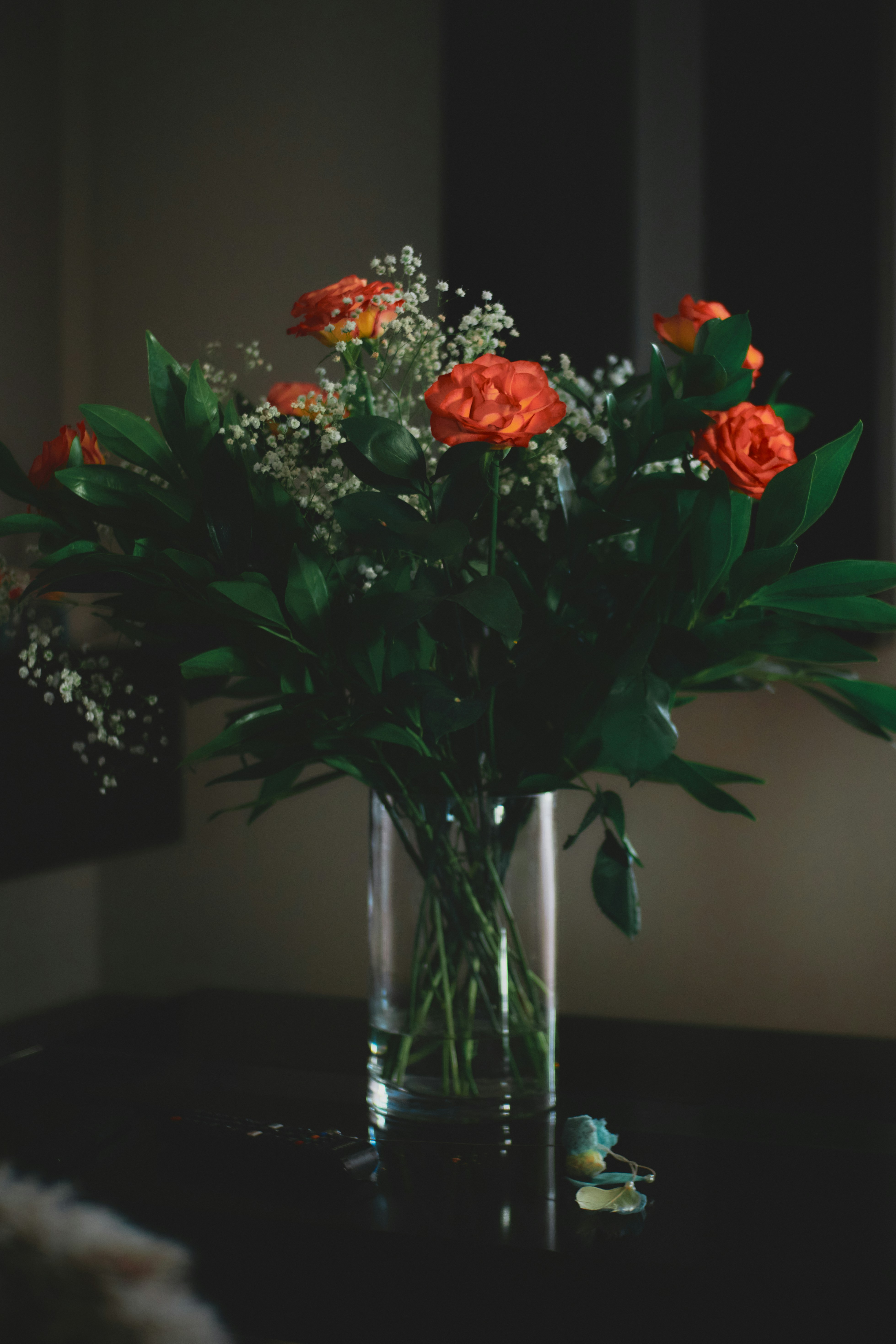Vibrant orange roses surrounded by delicate greenery in a clear glass vase on a dark wooden table.