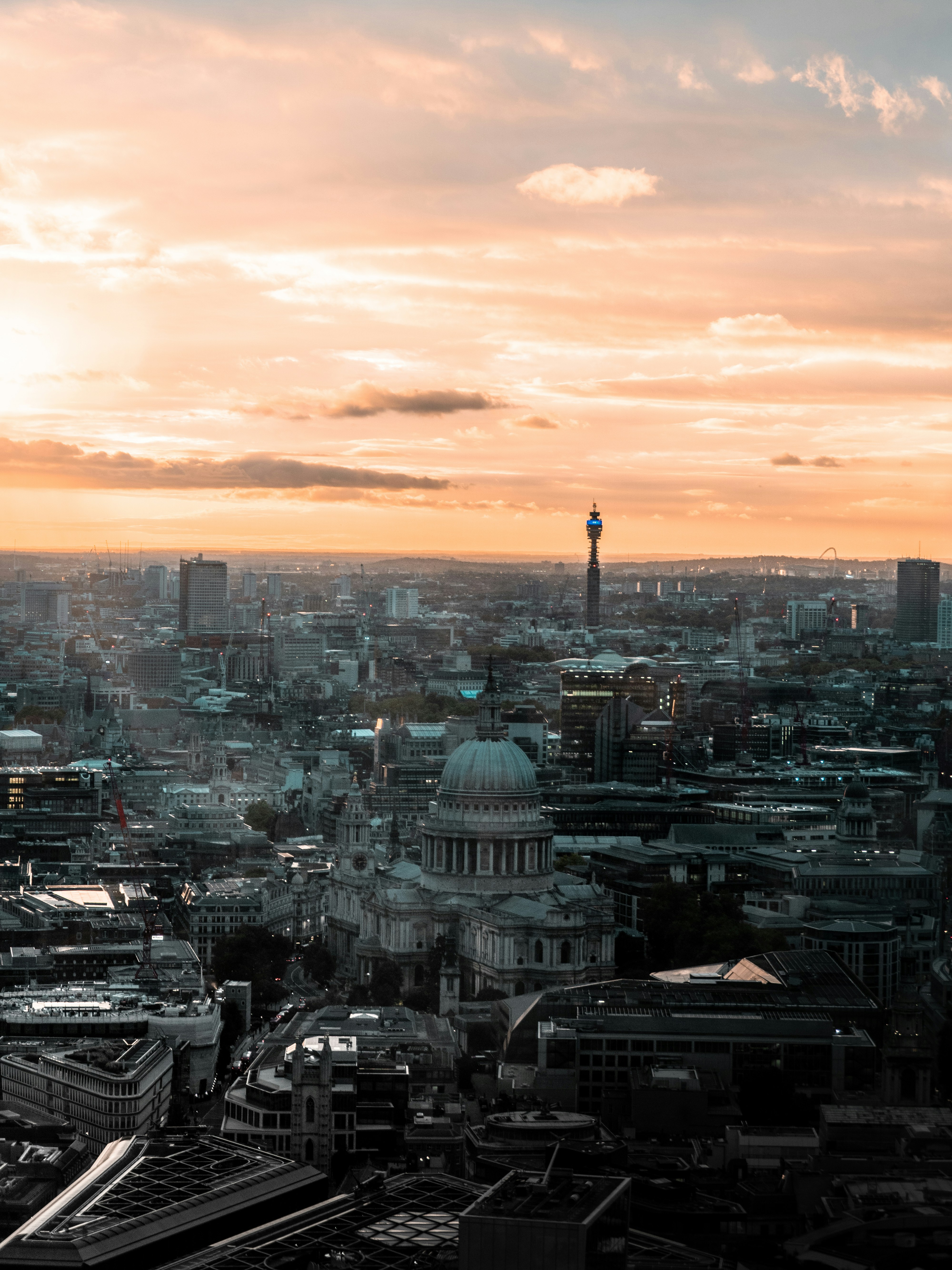 Panoramic view of a city skyline during sunset, featuring notable architectural landmarks silhouetted against a colorful sky.