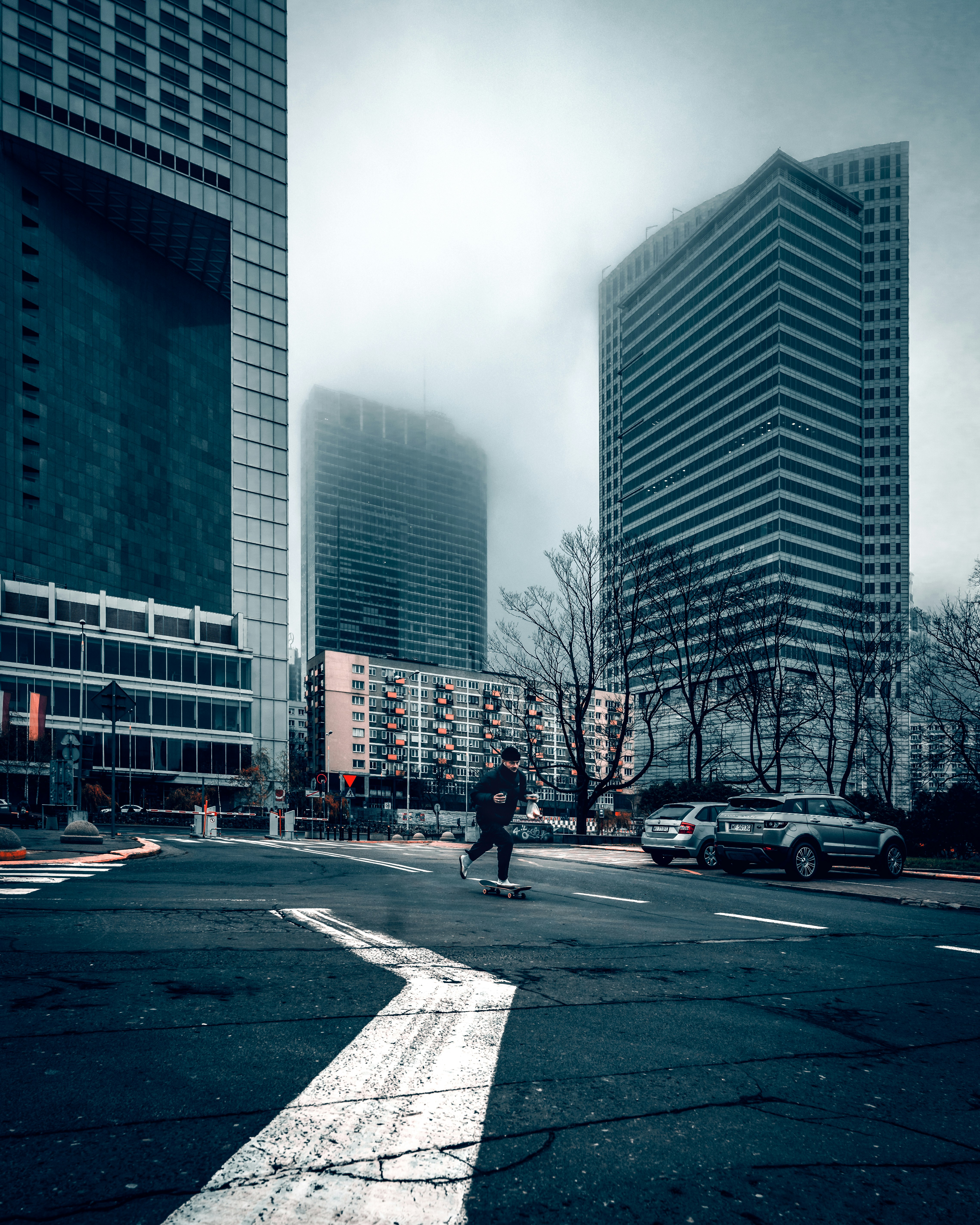 Misted Crosswalk: A skateboarder's dash beneath fog-wreathed towers