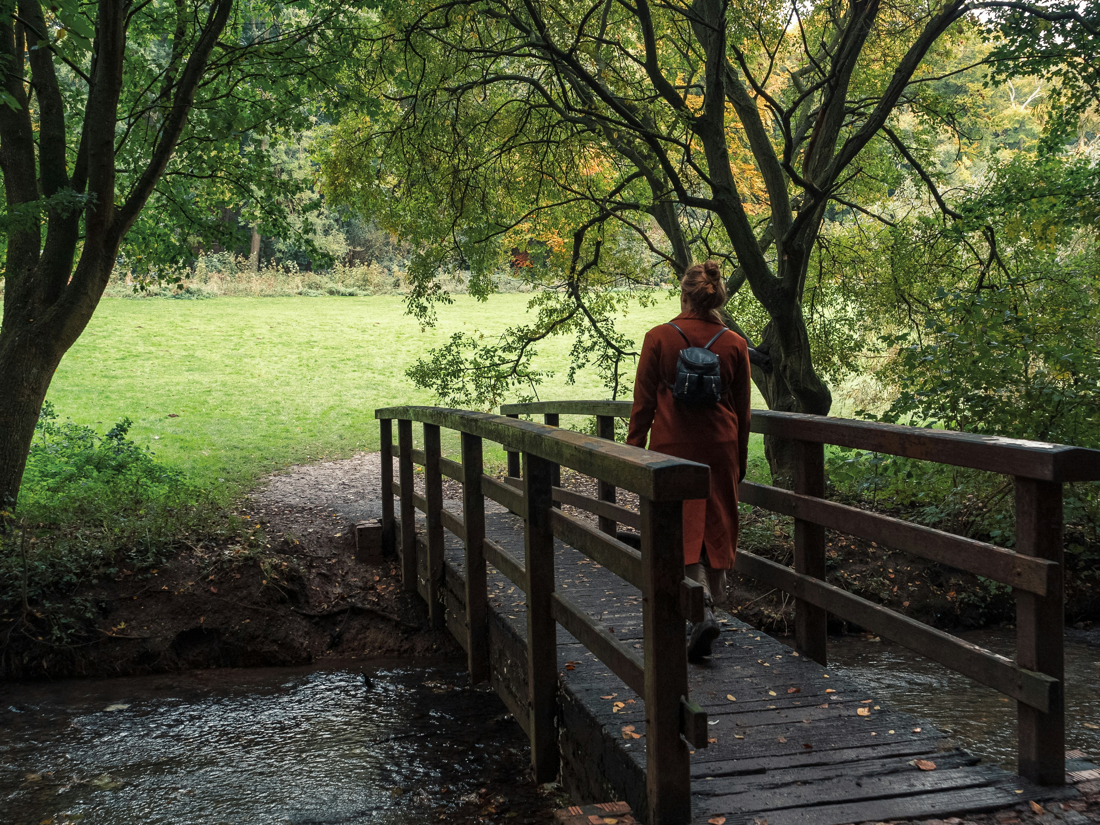 woman in red dress standing on brown wooden bridge over river during daytime