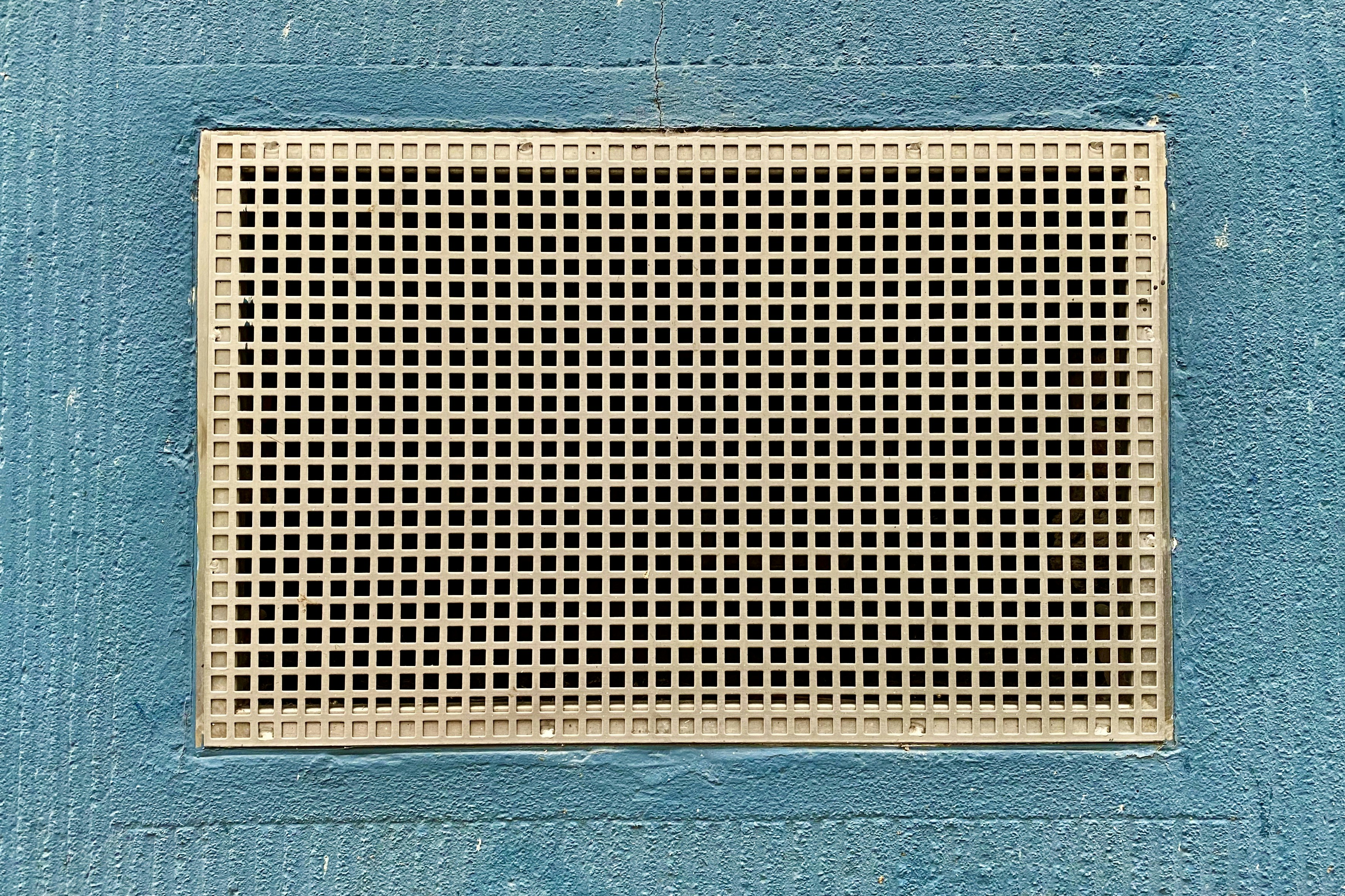 A textured ventilation grate set against a vibrant blue wall, showcasing a grid pattern that contrasts with the surrounding surface.