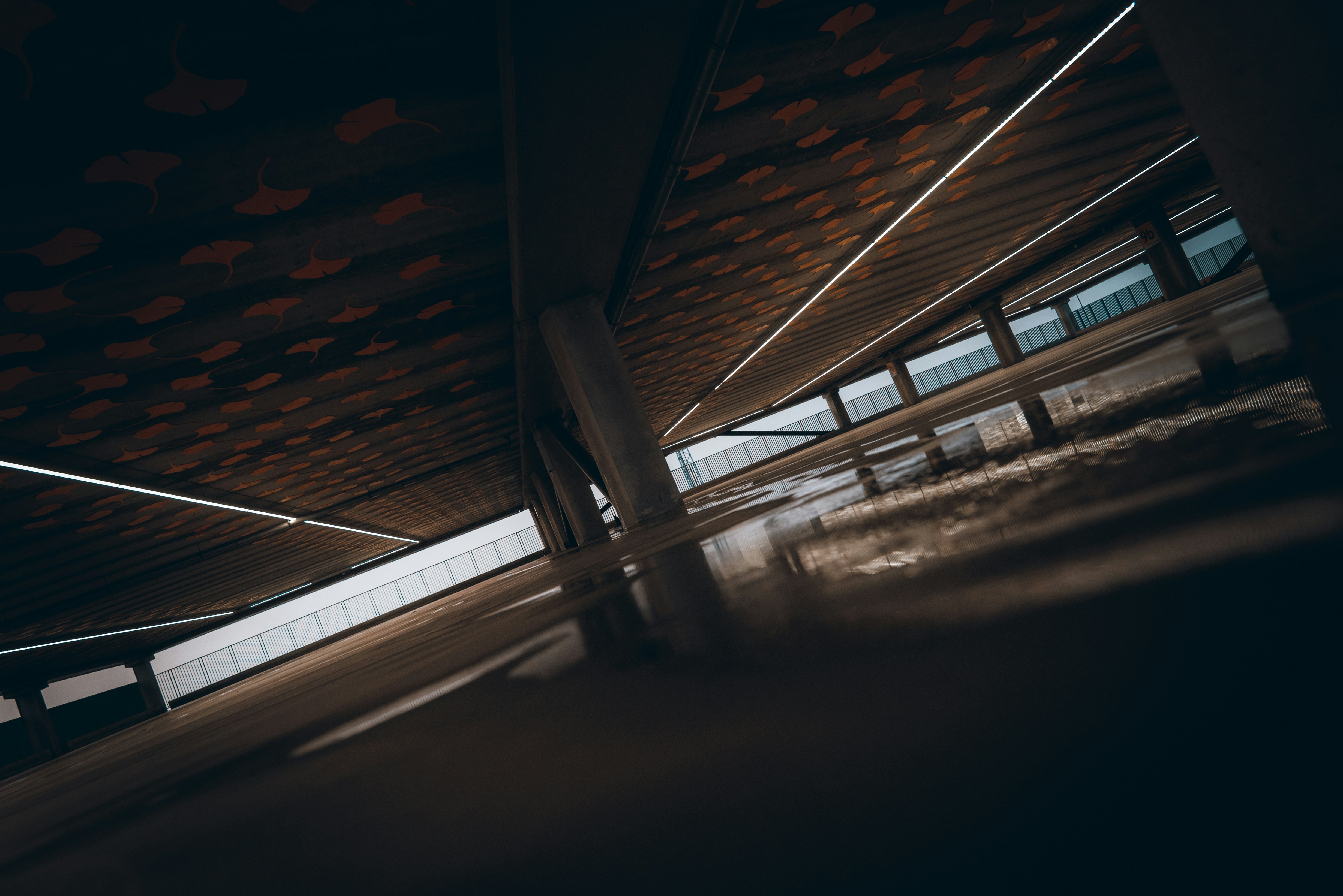 Abstract view of a parking structure's underside, showcasing geometric patterns and reflections on wet concrete.