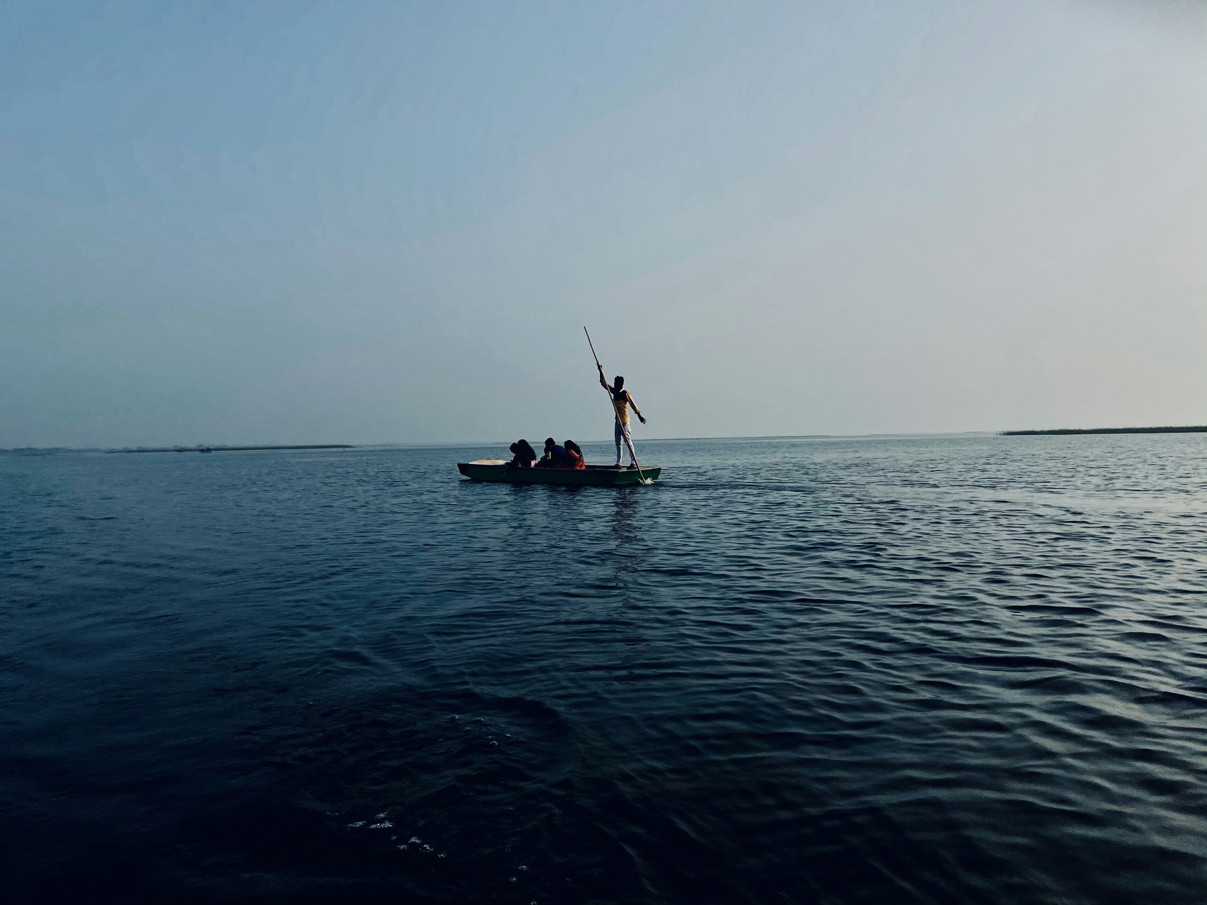 A lone boatman navigates a calm, expansive ocean under a clear blue sky.
