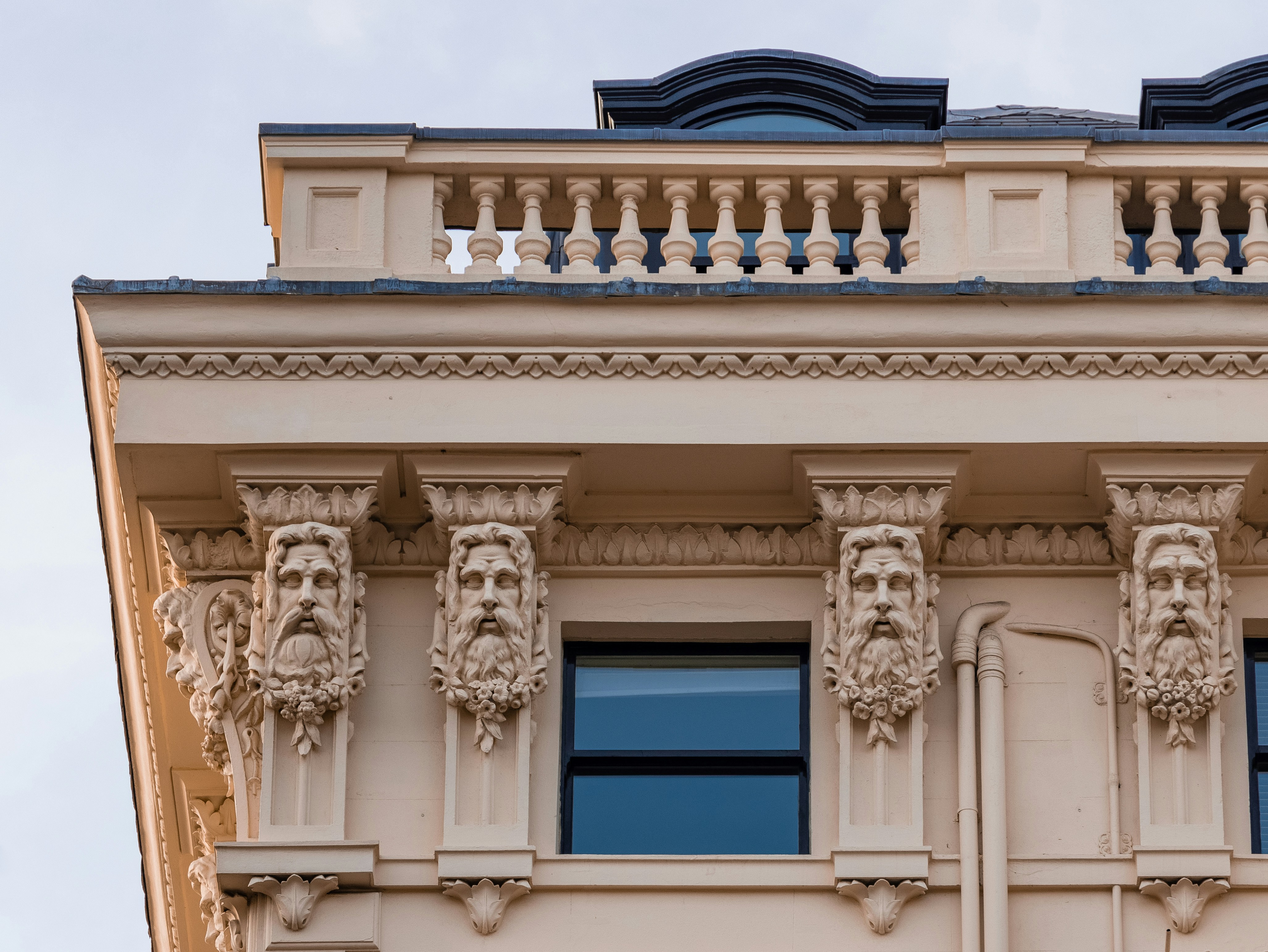 Intricate stone faces adorn the upper facade of a historic building, showcasing detailed craftsmanship and architectural grandeur.