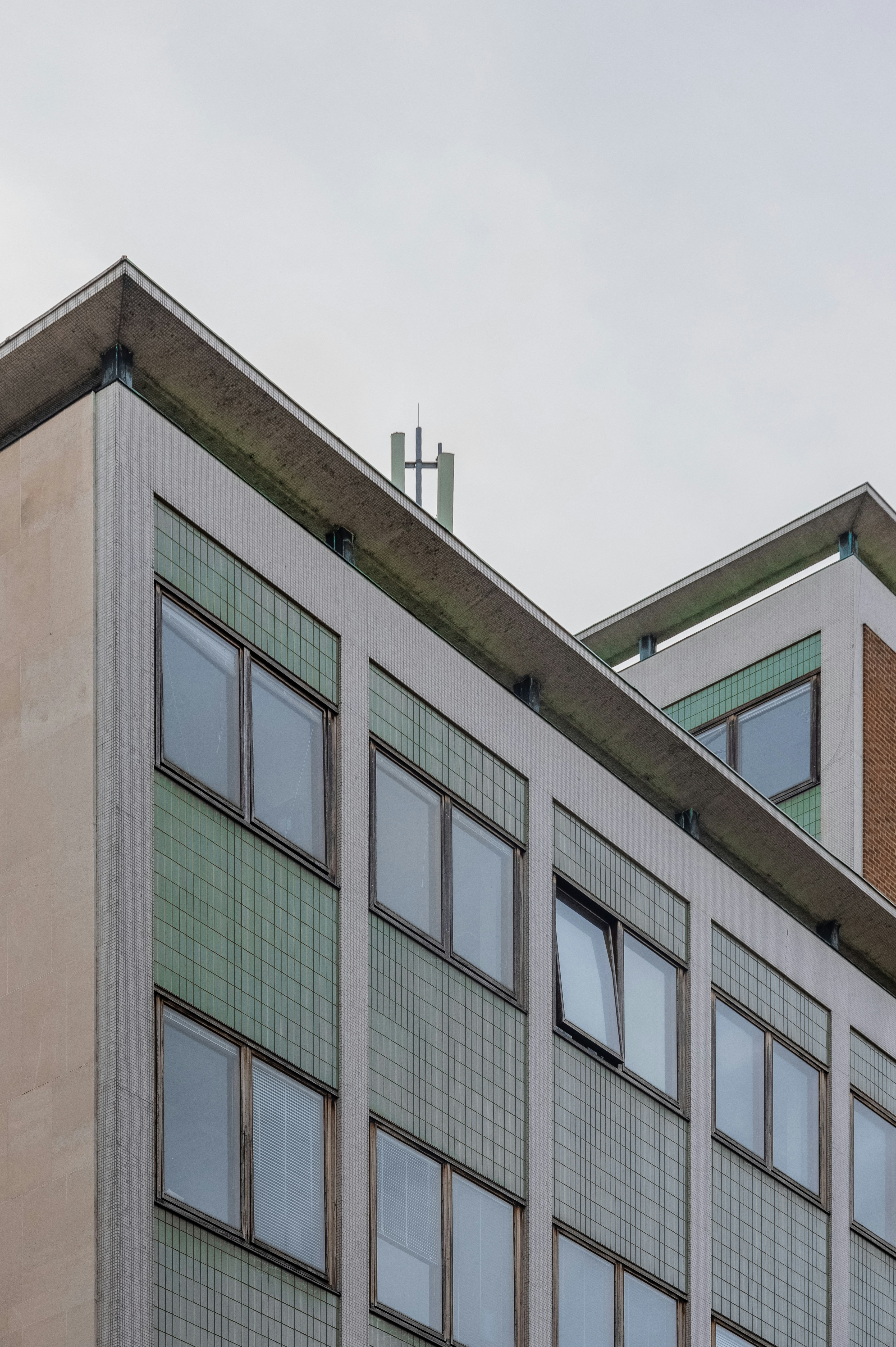 Modern building facade showcasing a mix of green tiles and large windows under a cloudy sky.