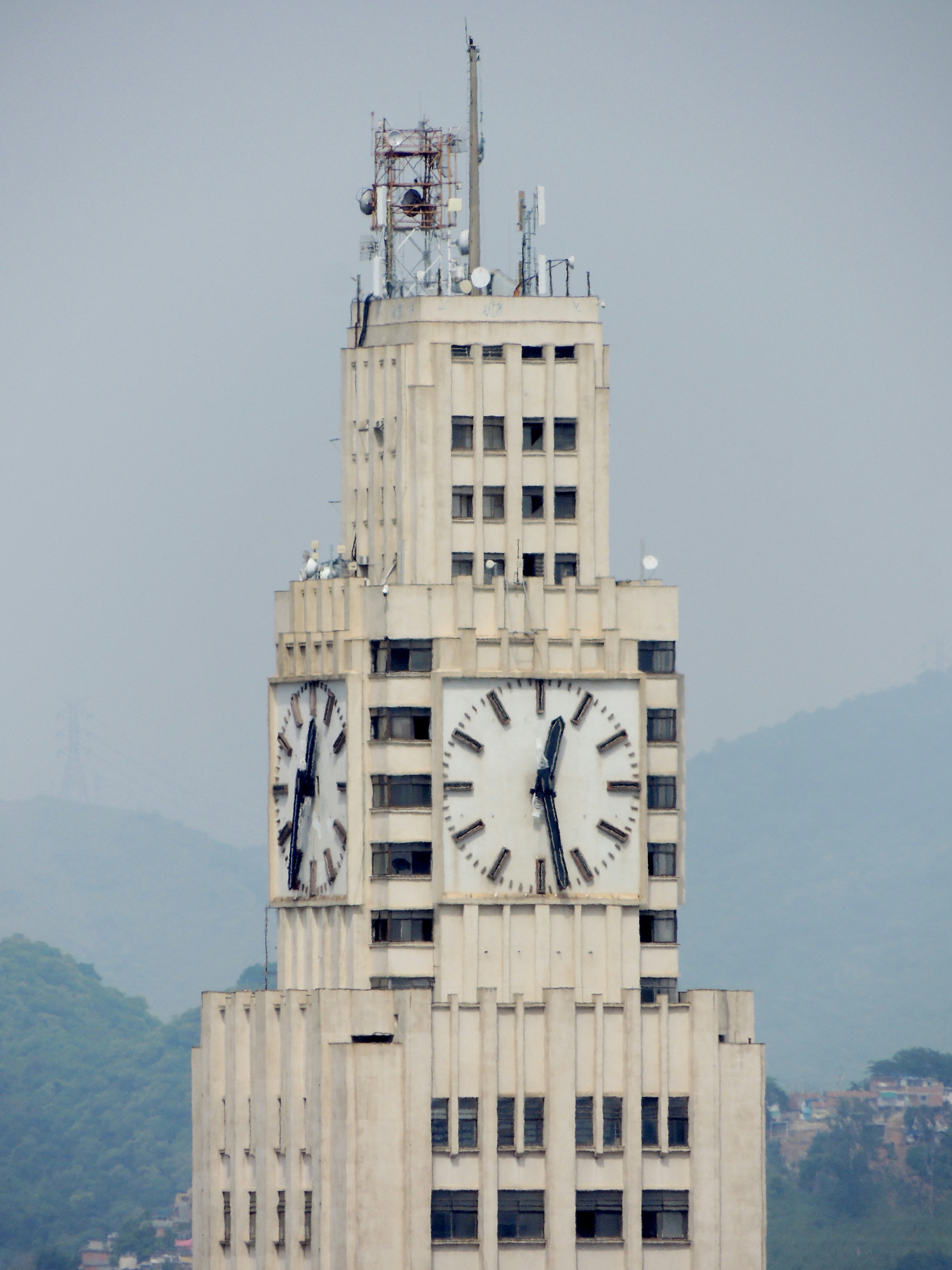 A historic clock tower stands tall against a misty backdrop, showcasing its intricate design and large clock faces. The structure is a notable landmark in the city.