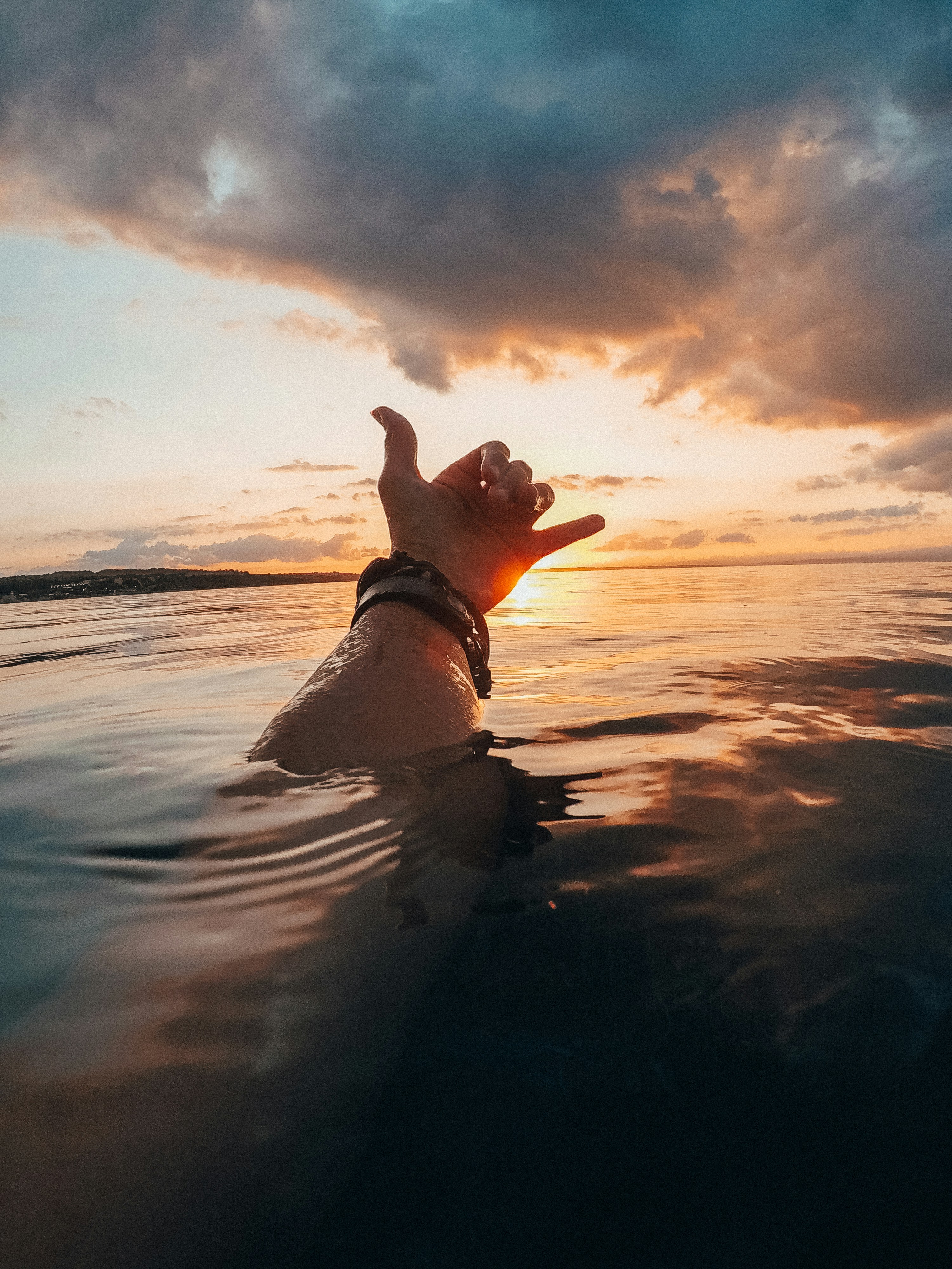 Hand reaching out from water towards a vibrant sunset, capturing a moment of tranquility and connection with nature.