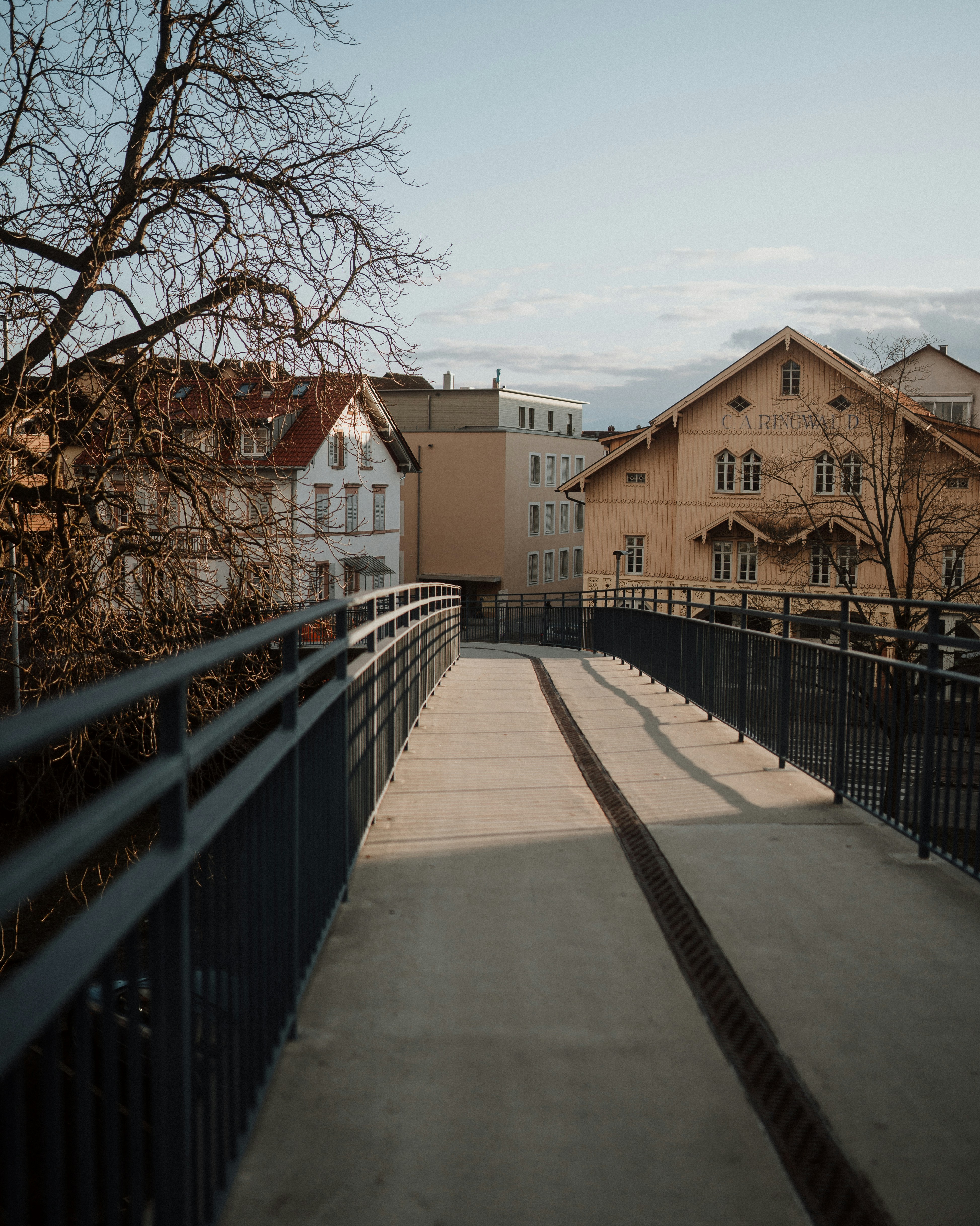 Modern pedestrian bridge leading through a quaint urban landscape with historical buildings and a clear sky.