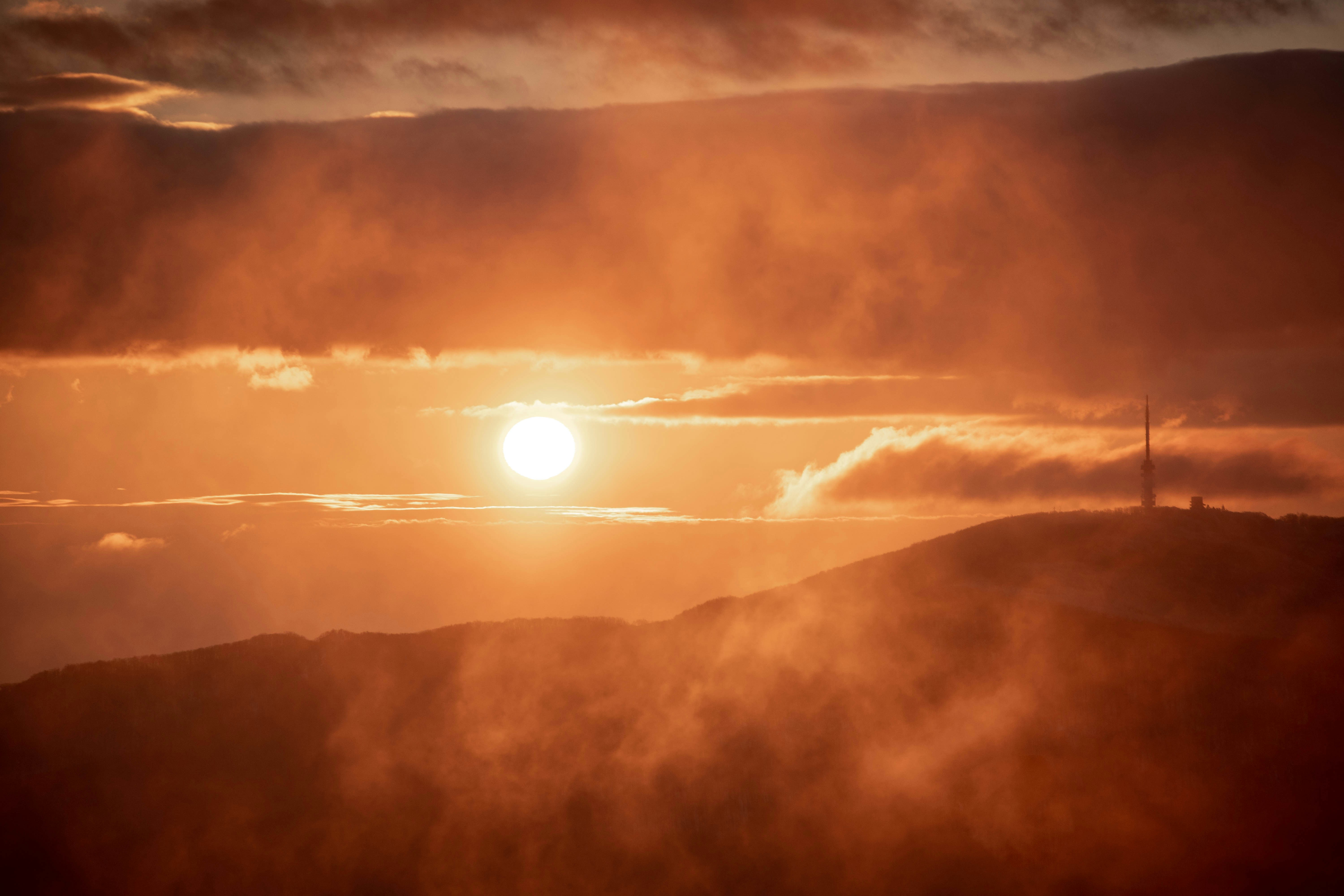 Golden sun rising over a misty mountain silhouette, with a communication tower peeking through the clouds. 